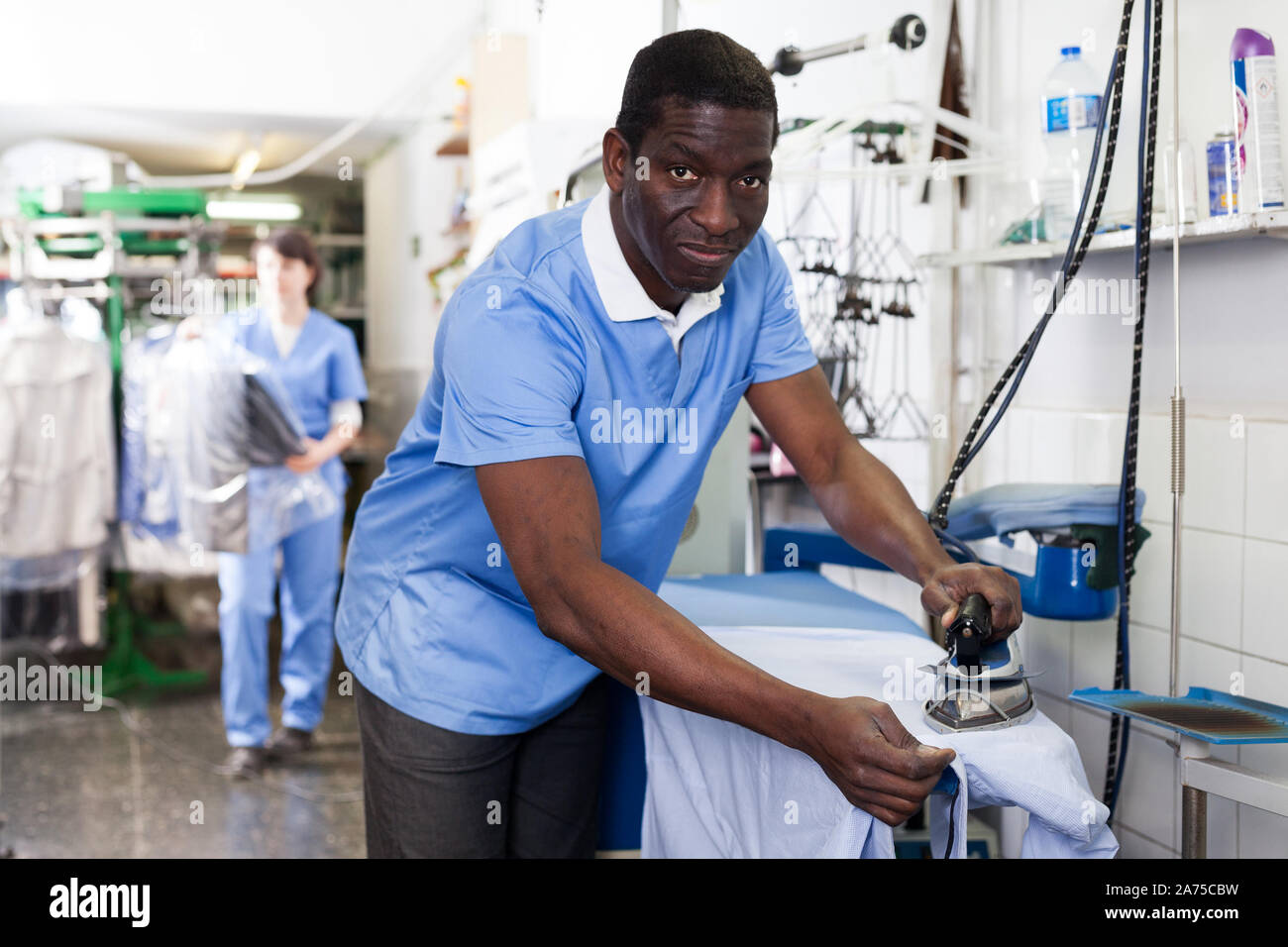 African-American man working in modern dry cleaning salon, ironing ...