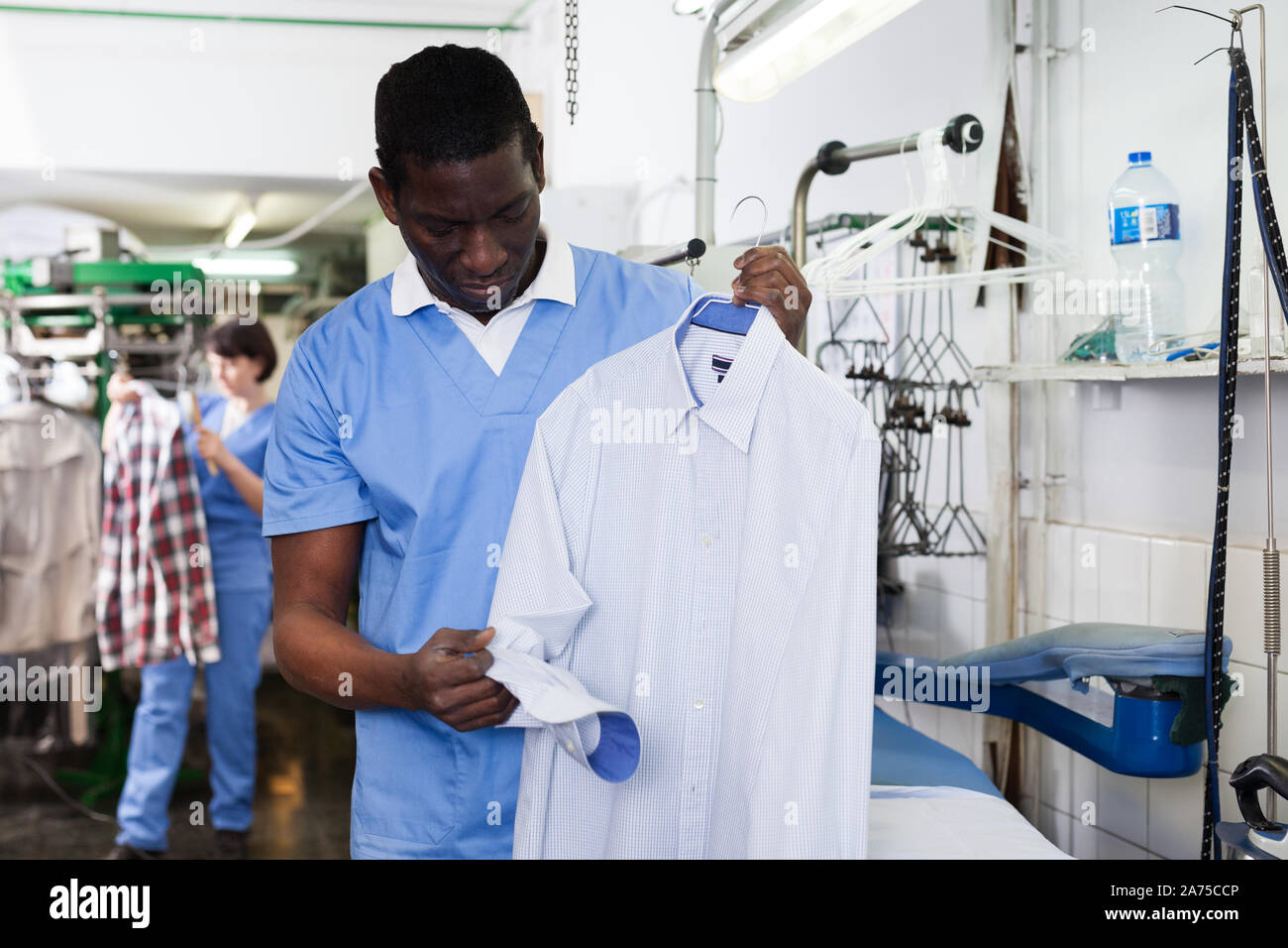 Focused African-American man working in modern laundry, checking ...