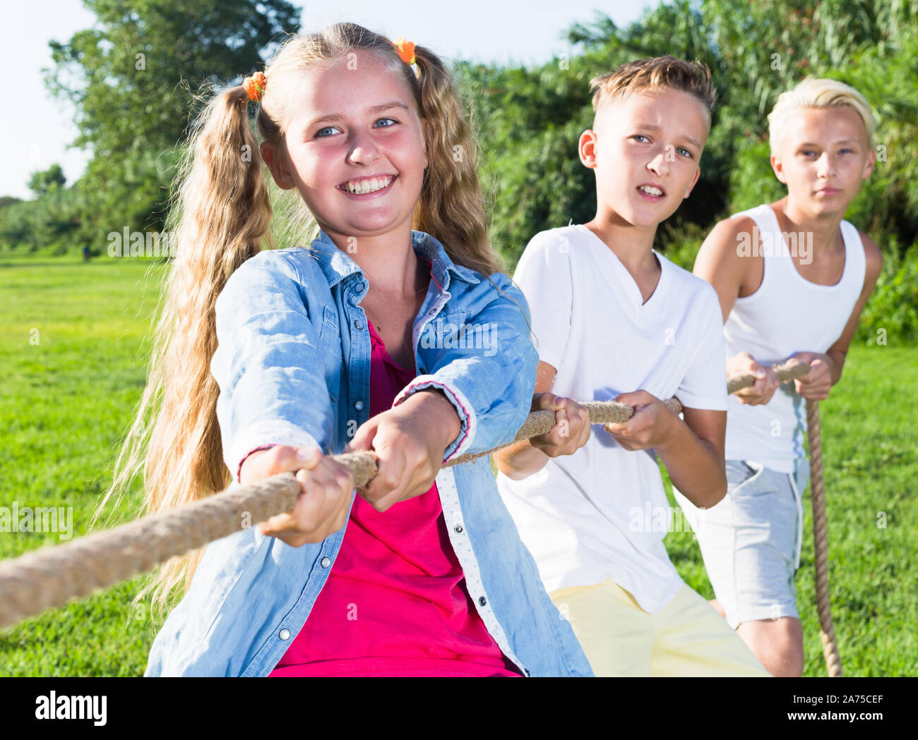 Group of laughing children having fun together outdoors pulling rope ...