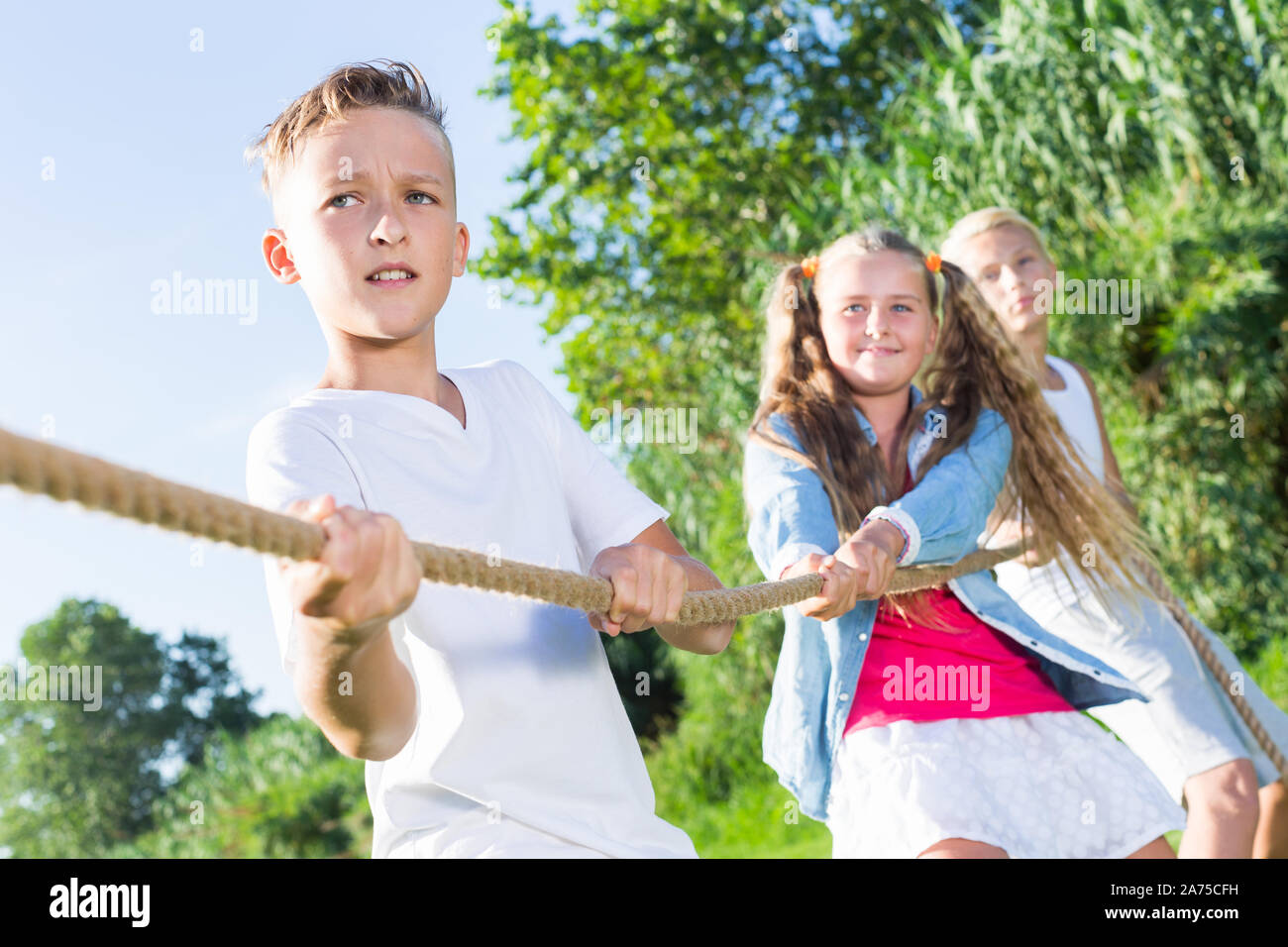 Group of laughing children having fun together outdoors pulling rope ...