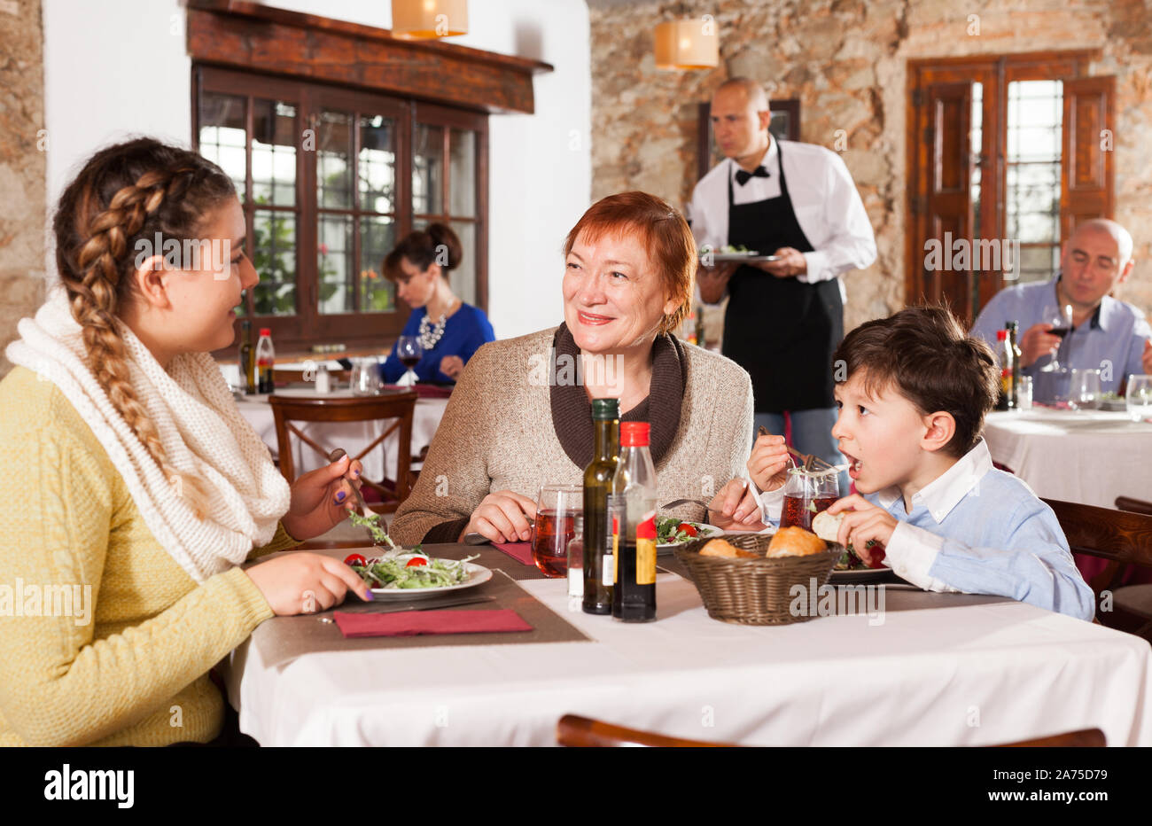 Portrait of two happy women with little boy having dinner in restaurant ...