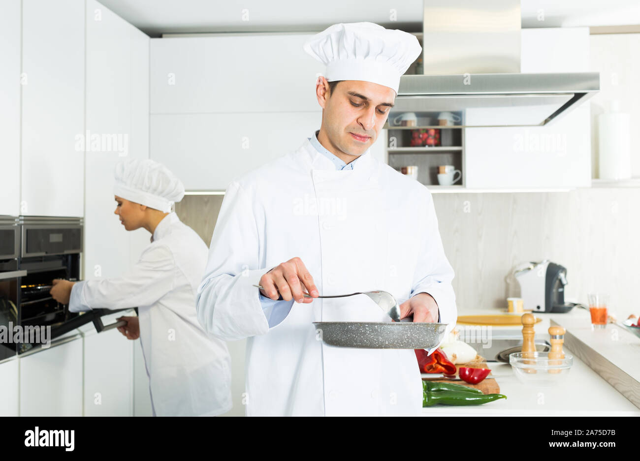 Male cook wearing uniform with stewpot working on kitchen with woman ...