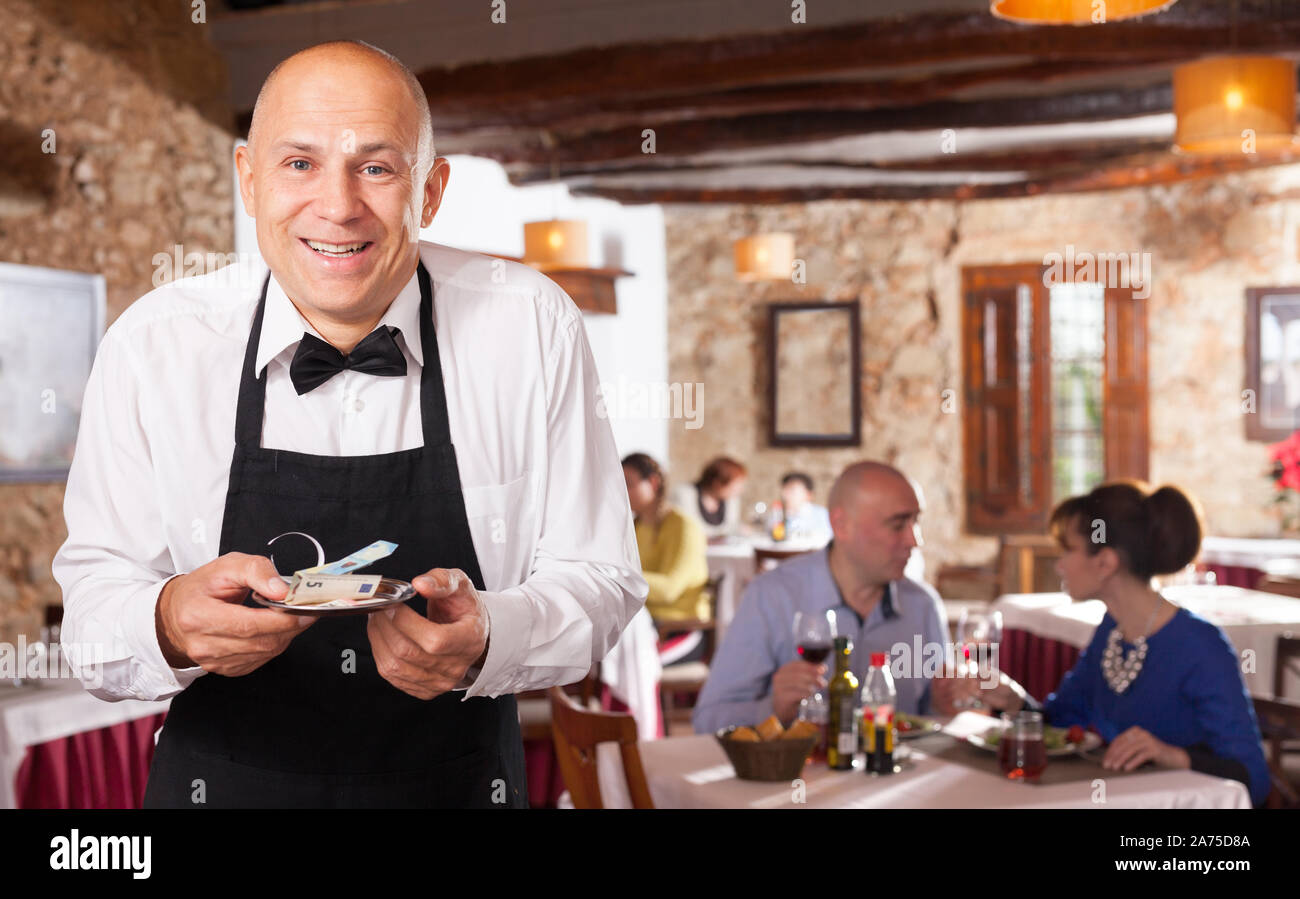 Portrait of happy waiter in white shirt and black apron holding good ...