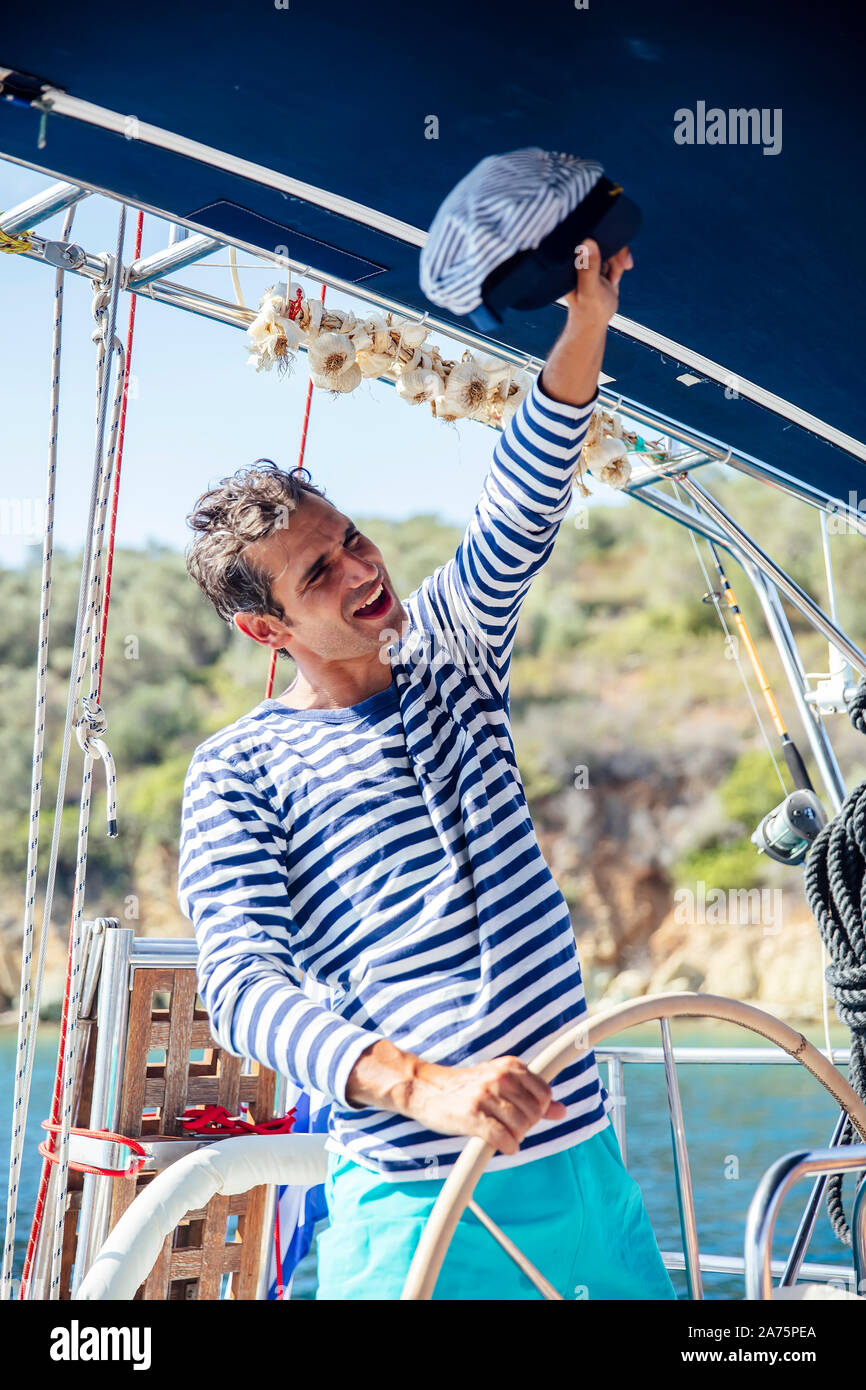 Handsome young man with captain cap on a sailboat at sea on a suuny day ...