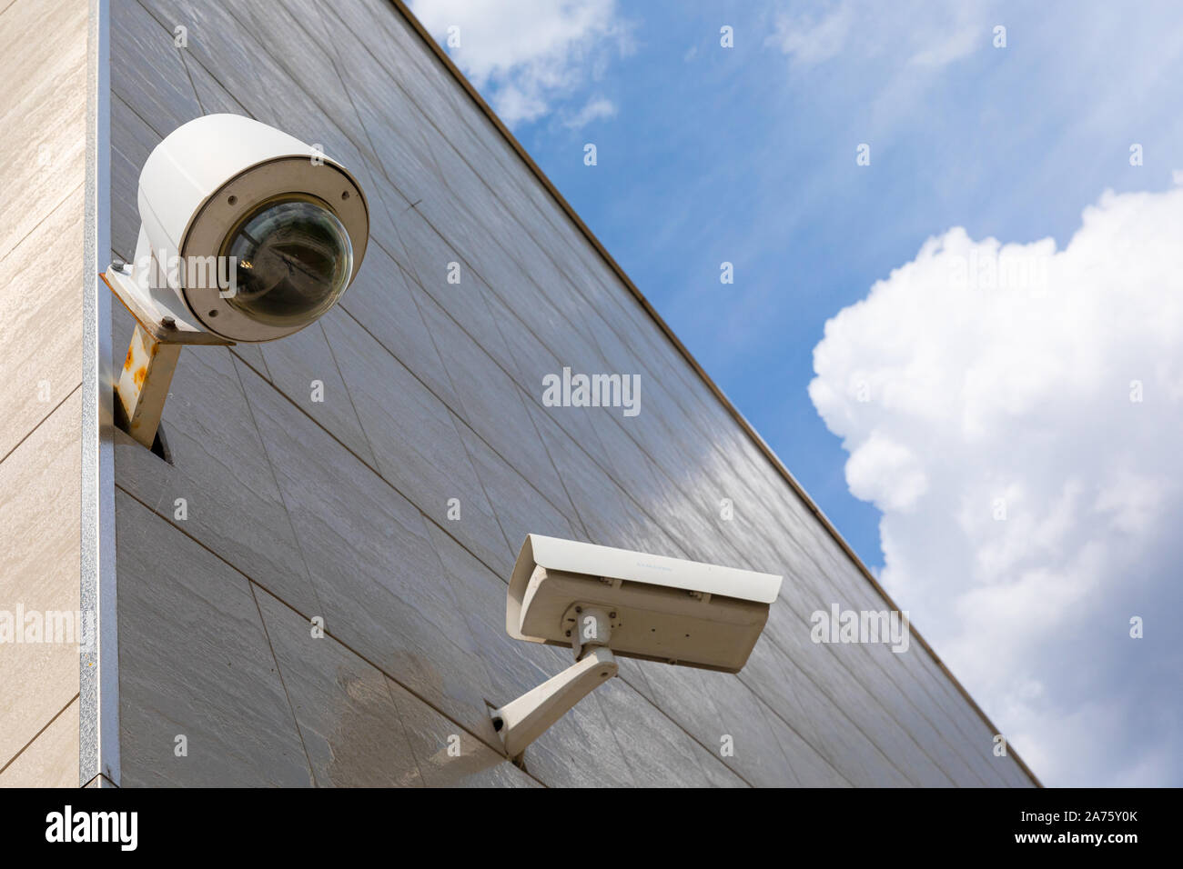 Safety camera device and lamp on tiled gray building wall on cloudy sky ...