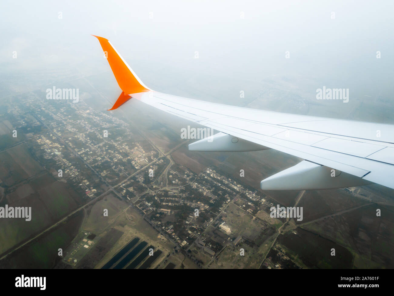 wing of a flying civil airliner over a city and fields Georgia Tbilisi ...