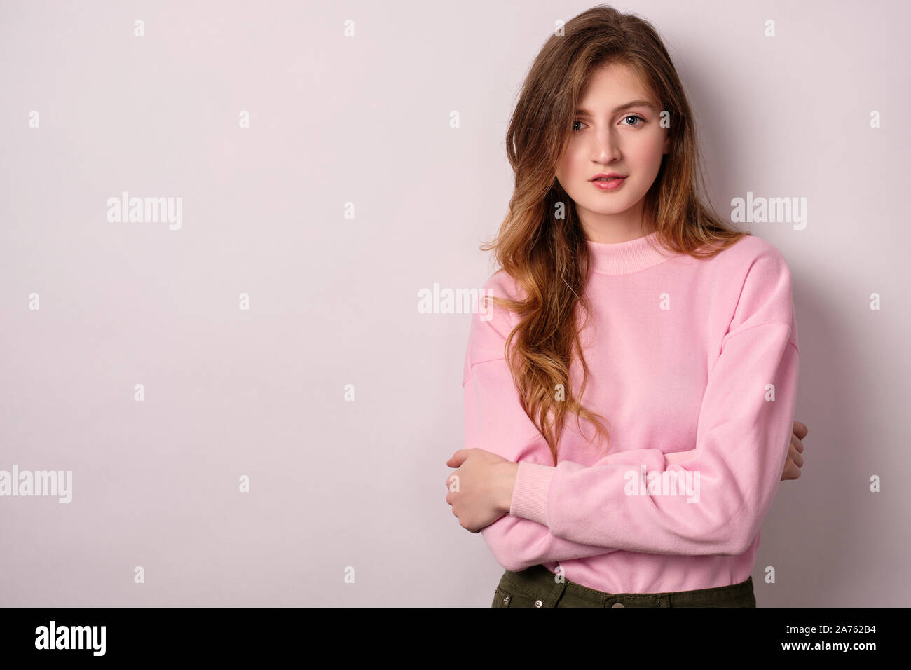 A girl in a pink sweater stands on a white background, hugging herself ...