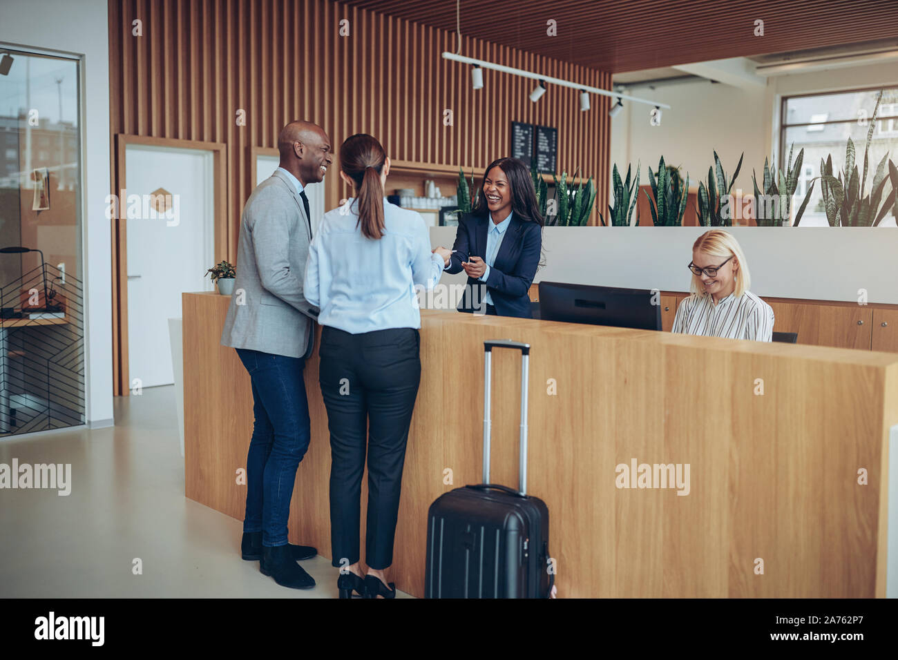 Two smiling guests talking to a concierge while checking in together at ...