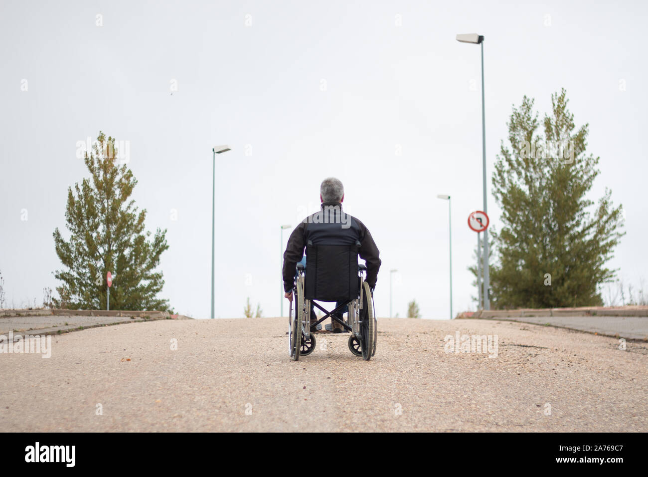 Rear vision of a disabled man in a wheelchair alone in the middle of ...