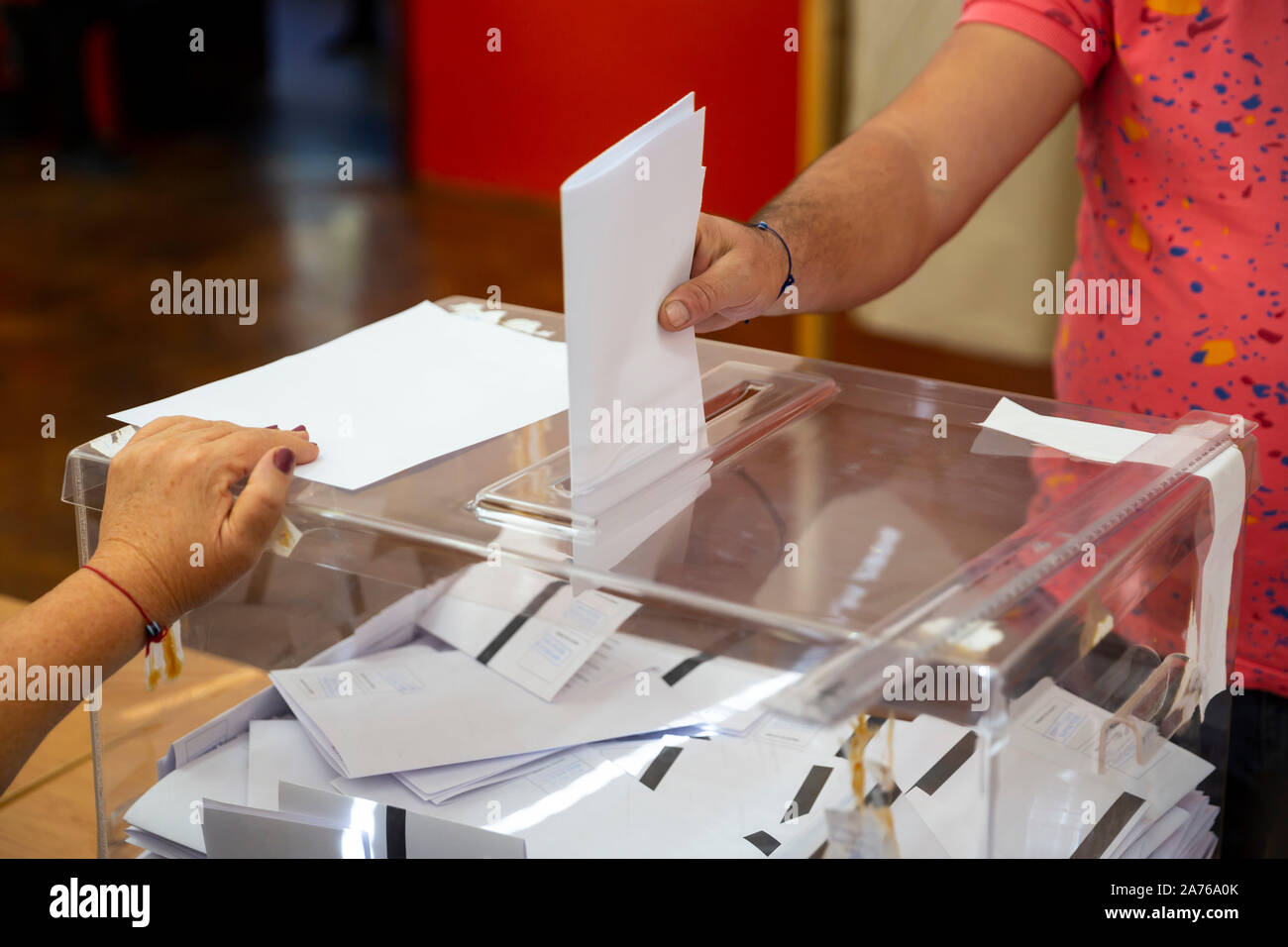 A man casts his envelope vote into a transparent plastic ballot box ...