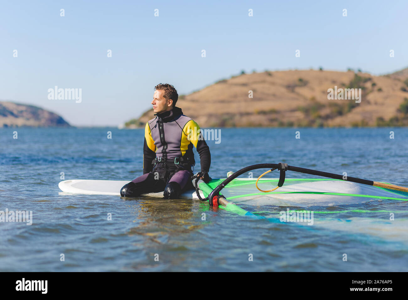 Portrait of windsurfer sitting on surfboard with sail in ocean Stock ...