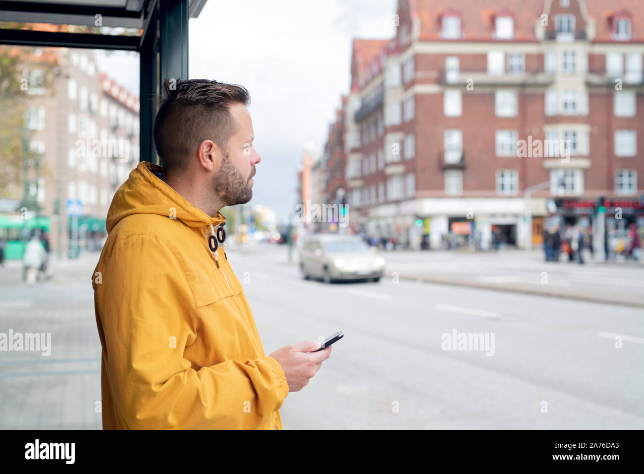 Man at bus stop with cell phone Stock Photo - Alamy
