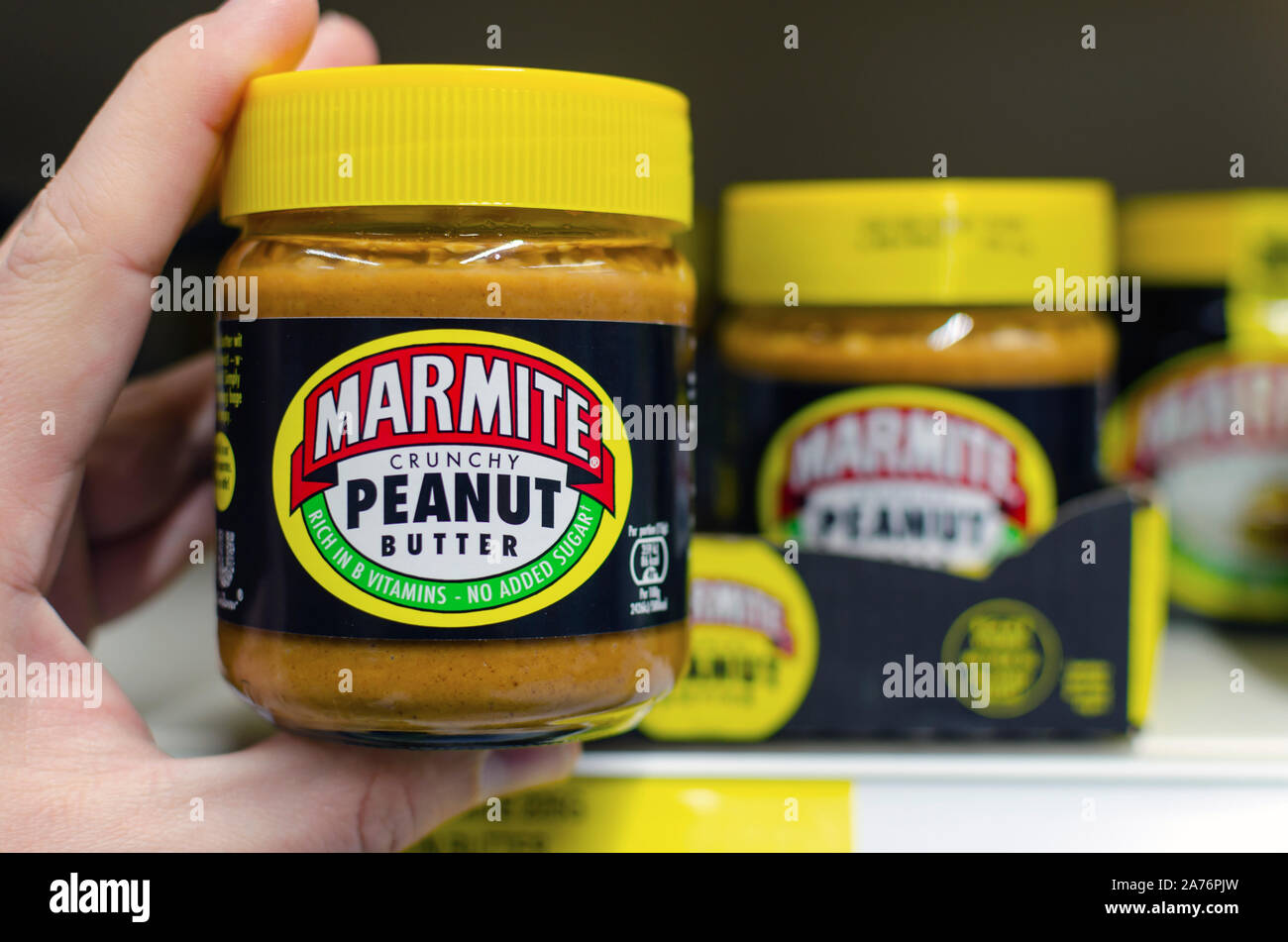 Marmite Peanut Butter jar hold in a hand next to supermarket shelf with ...