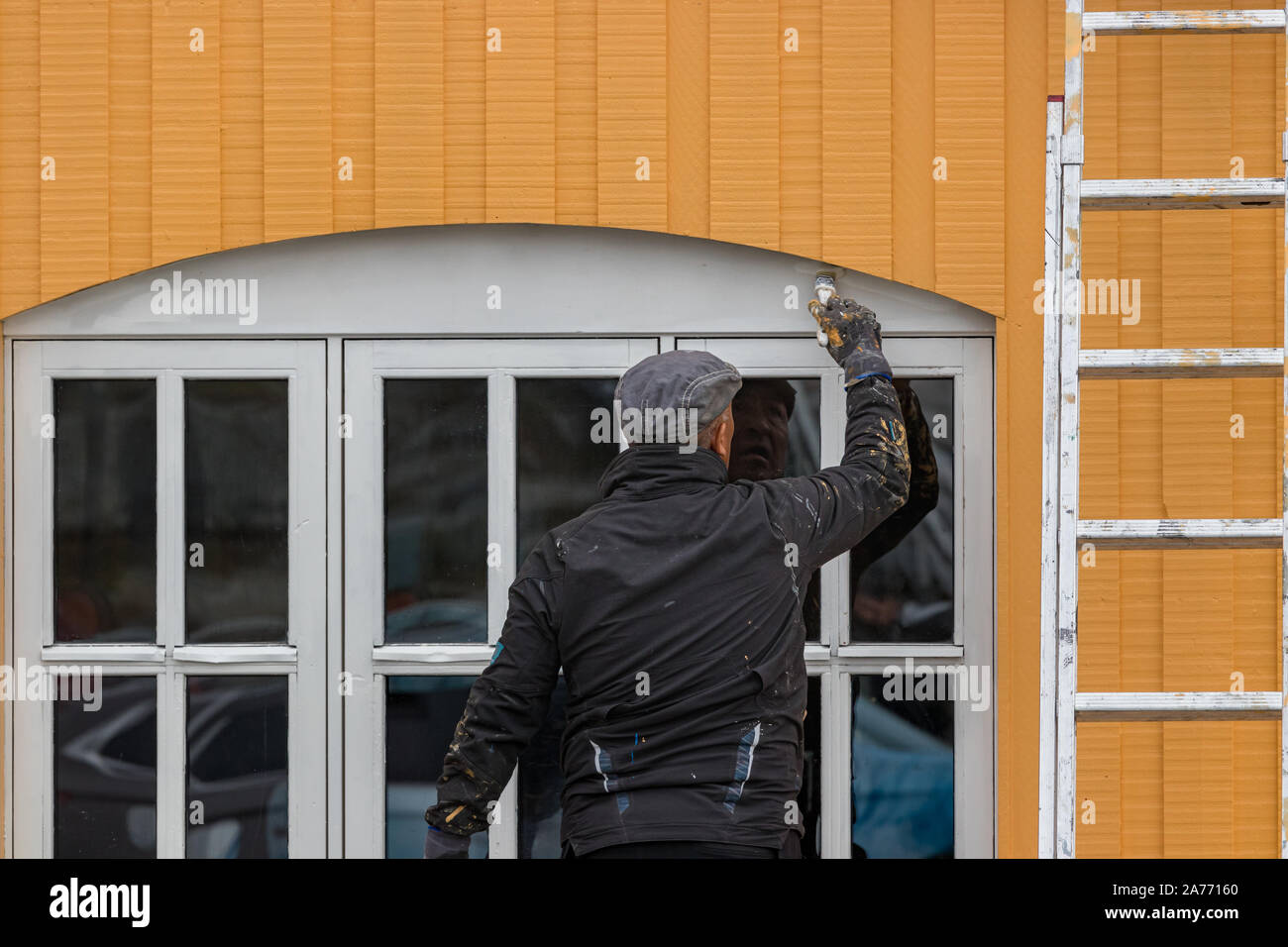 Inuit male worker painting a windows with a brush outdoors in Nuuk ...