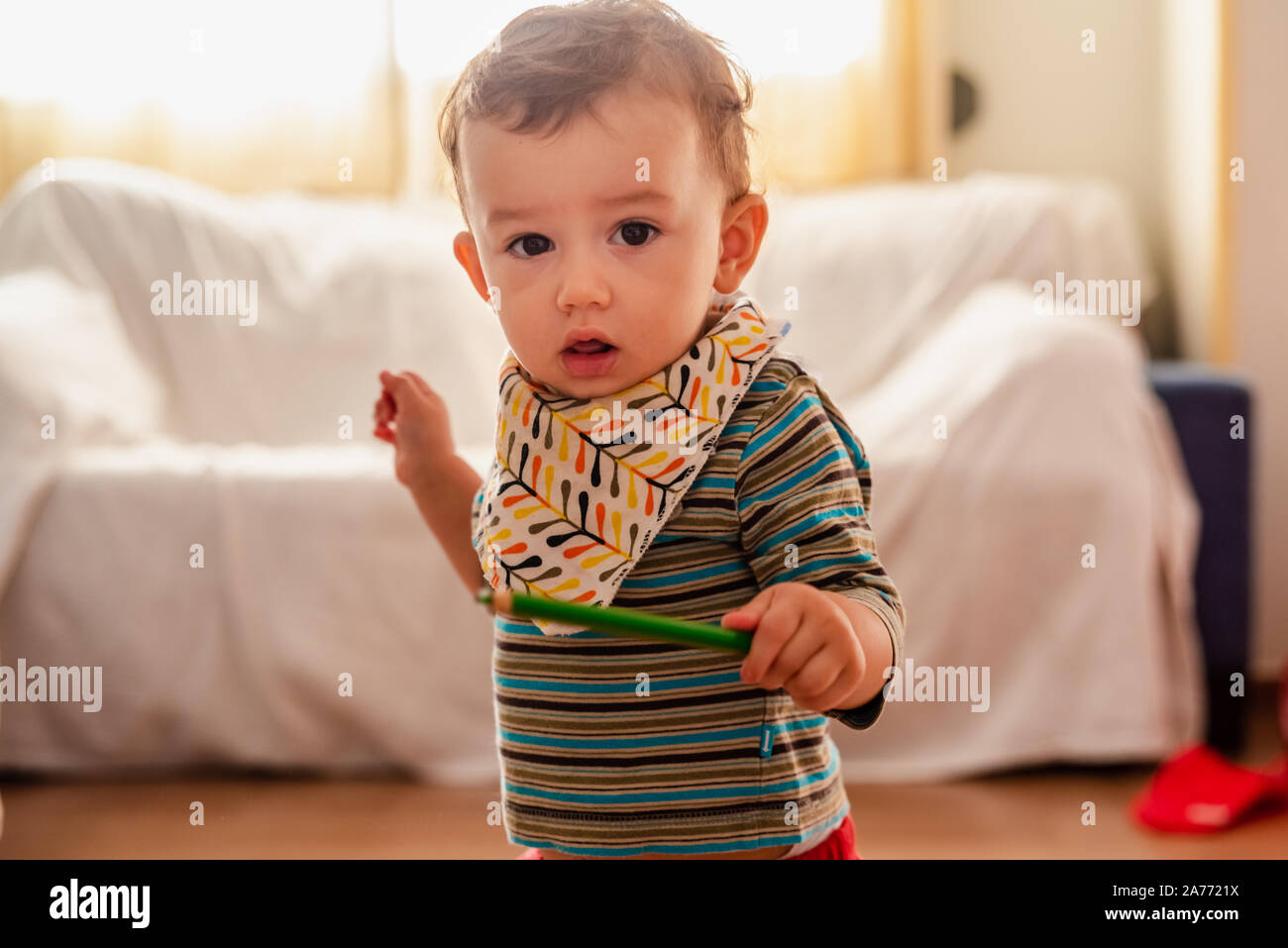Portrait of adorable 1 year old baby with bib and pencil in hand, at ...