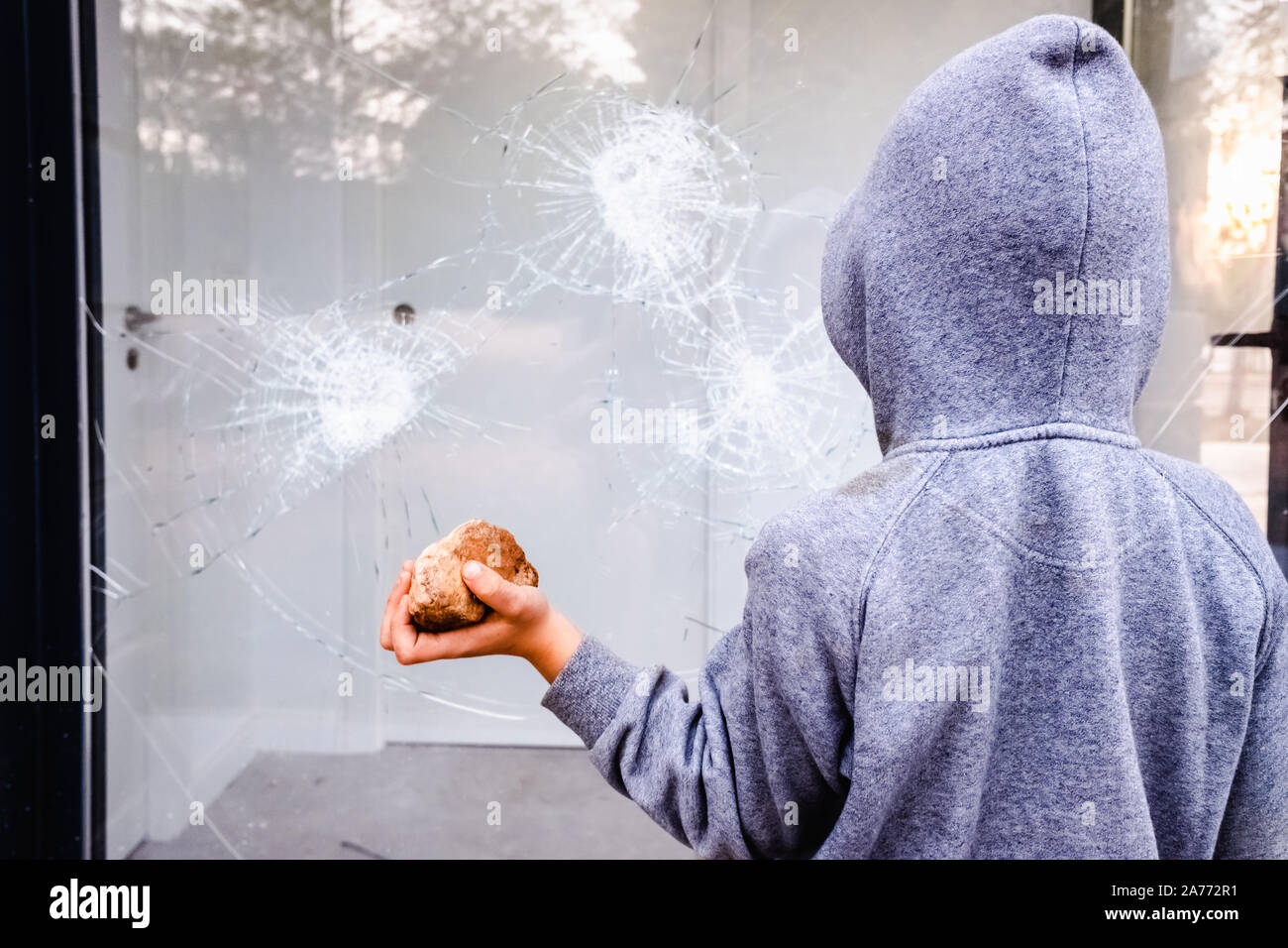 Protester holding a rock to break the glass of a shop window in the ...
