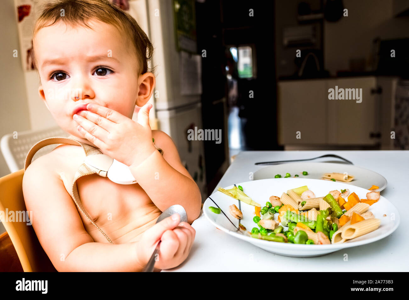 Baby with funny face enjoying his food eating with his hands making a ...