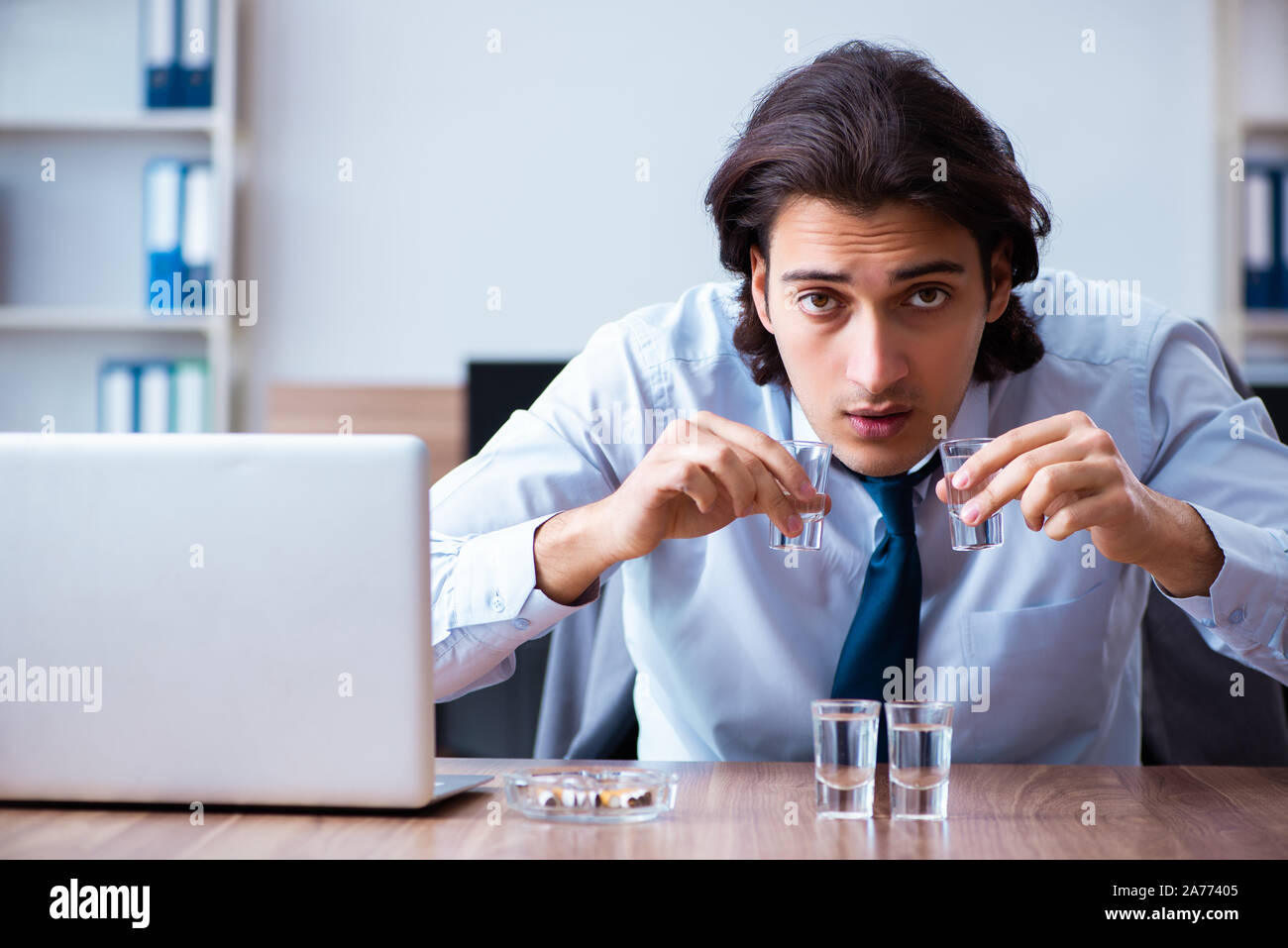 The male employee drinking vodka and smoking cigarettes at workplace ...