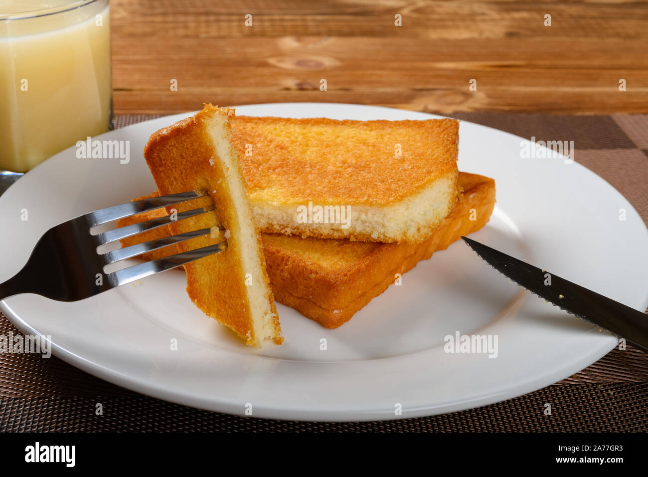 side view man eating toast with fork and knife and cup of soy milk ...