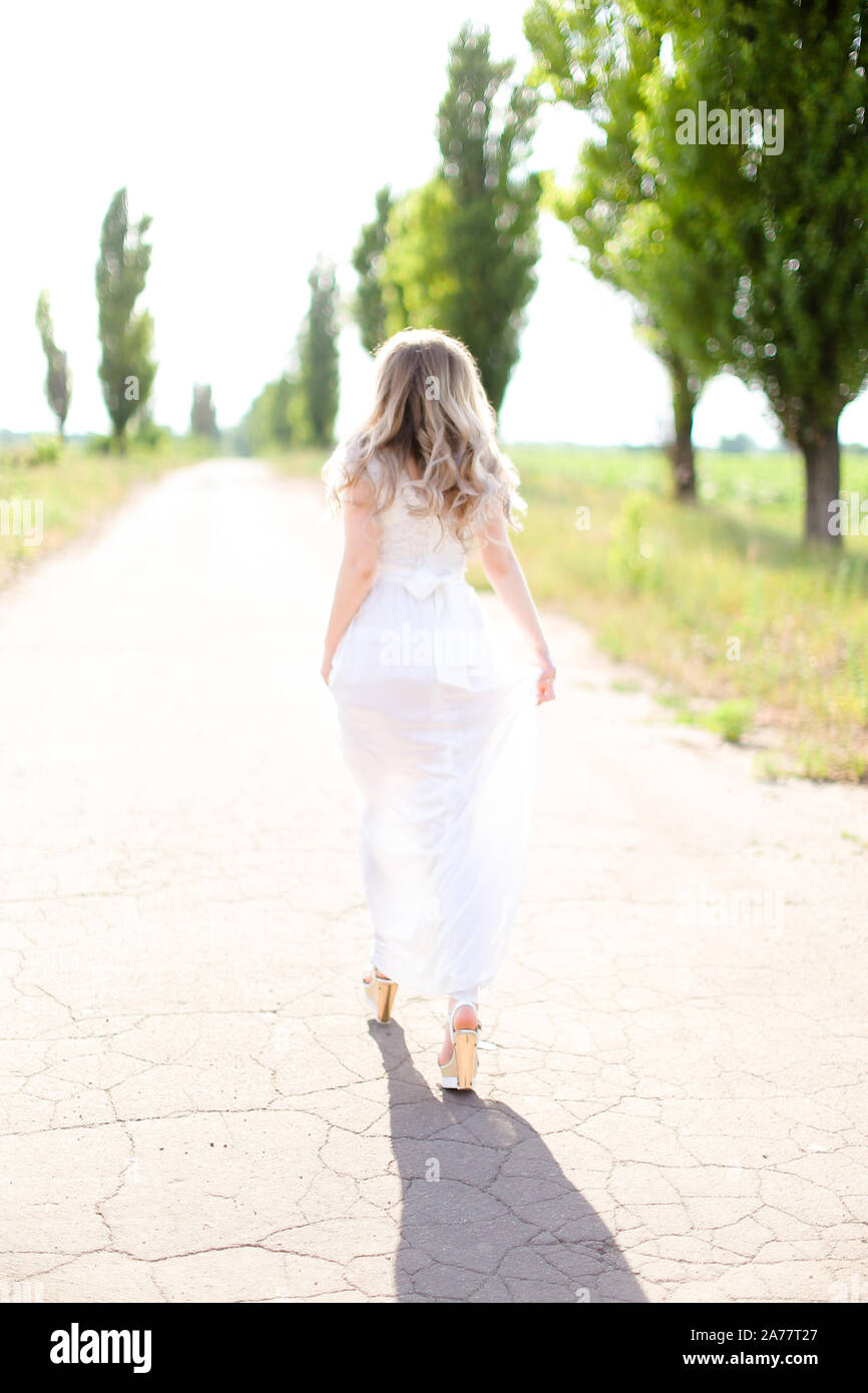 Back view of caucasian woman wearing white dress walking on road Stock ...