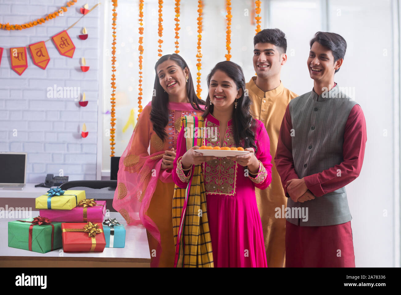 Employees standing together in office holding a plate of sweets during ...