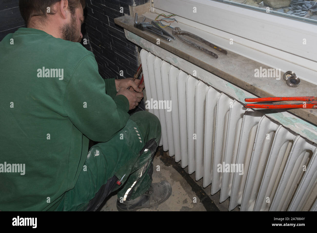Plumbing or heating plumber dismantles an old finned tube radiator ...