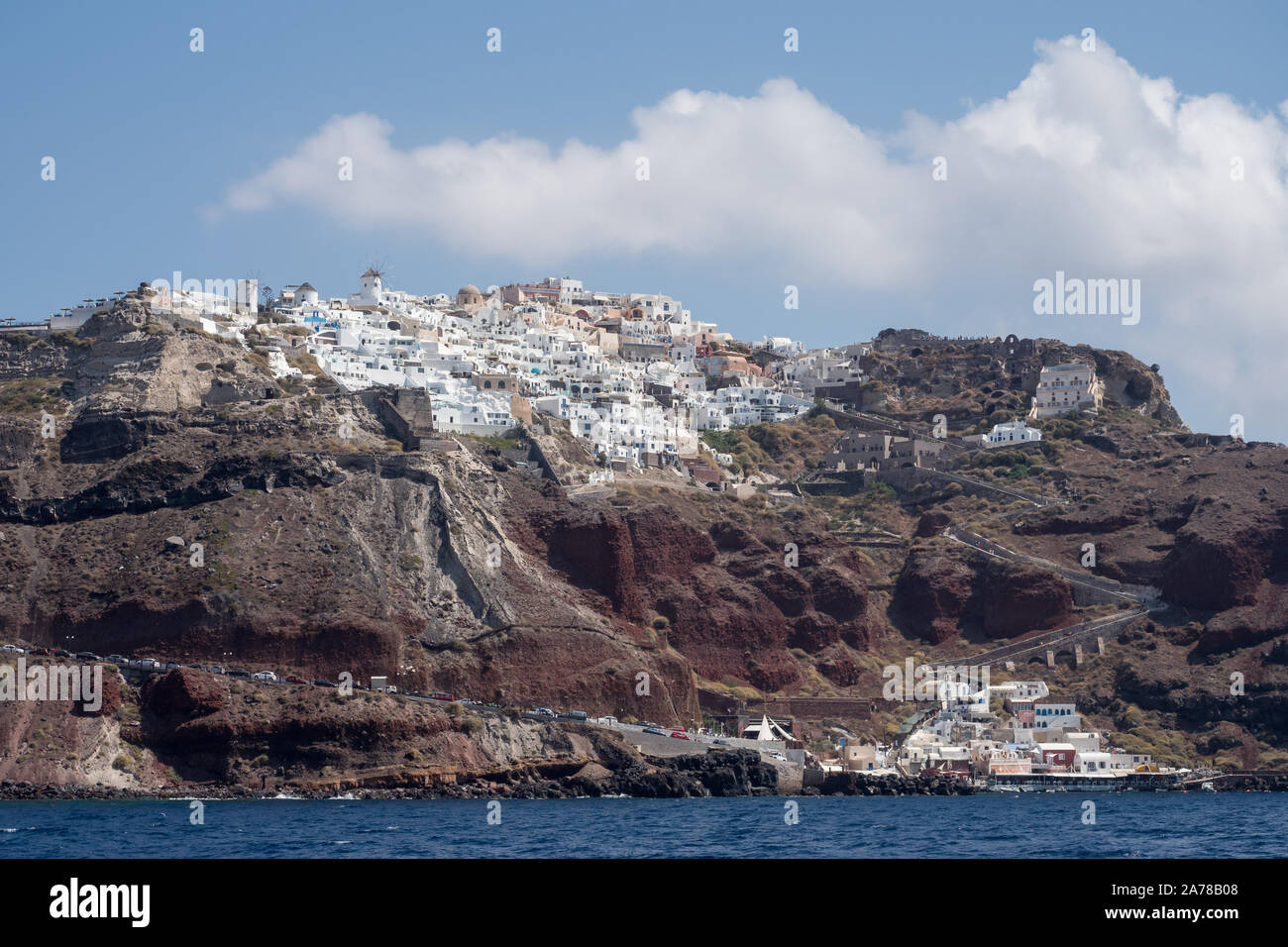 a view from below looking up at Oia on volcanic strata lava cliff top ...
