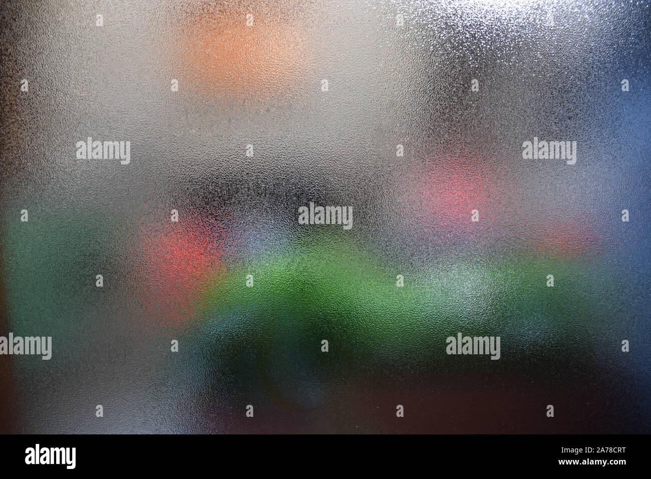 Closeup view of a grainy glass with colorful spots visible behind it ...