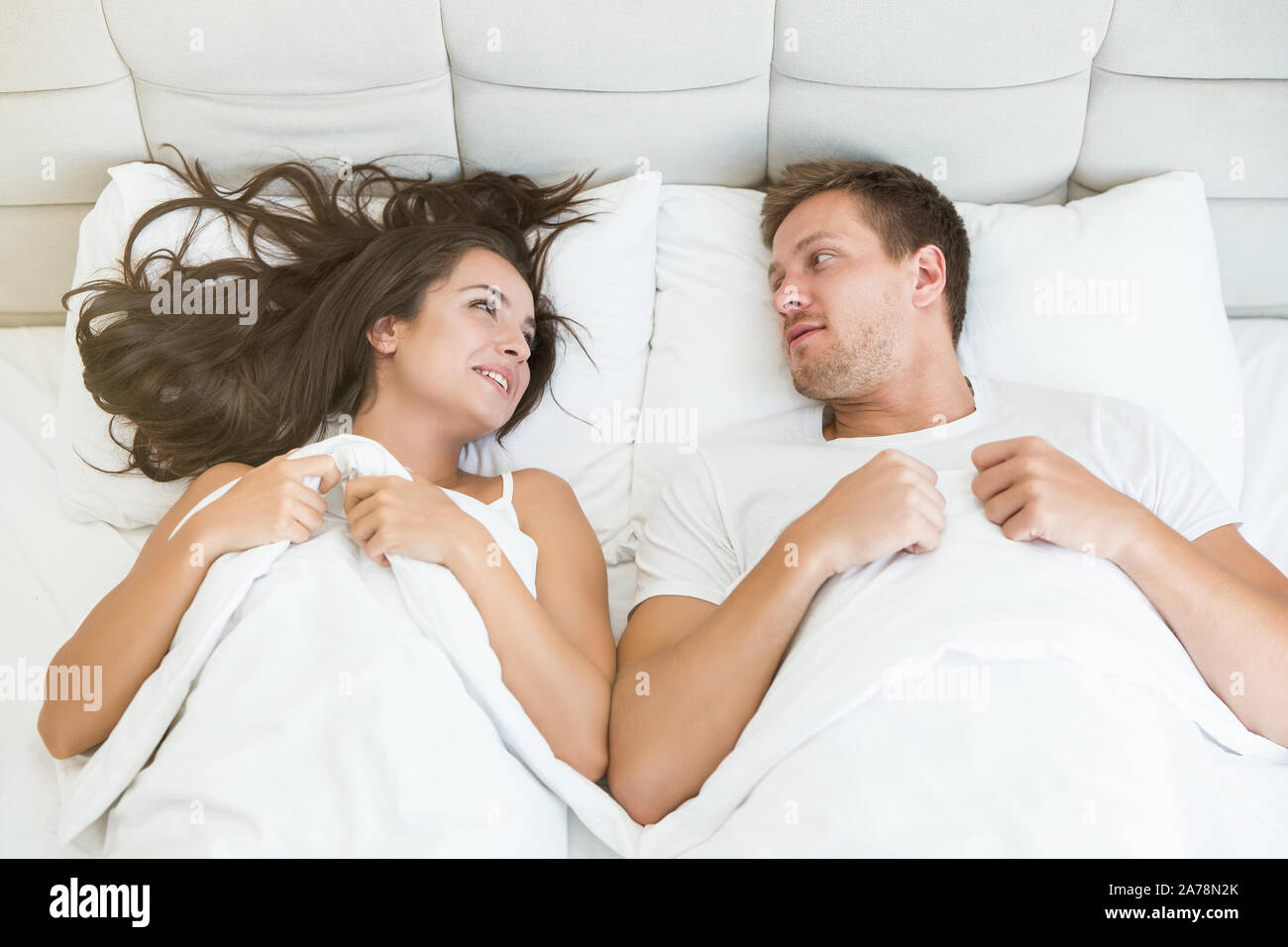 young couple handsome husband and beautiful wife lying in bed in bright ...
