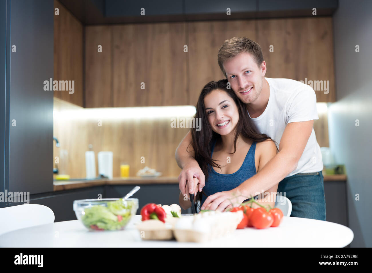 young couple cooking breakfast in the kitchen husband stands behind and ...