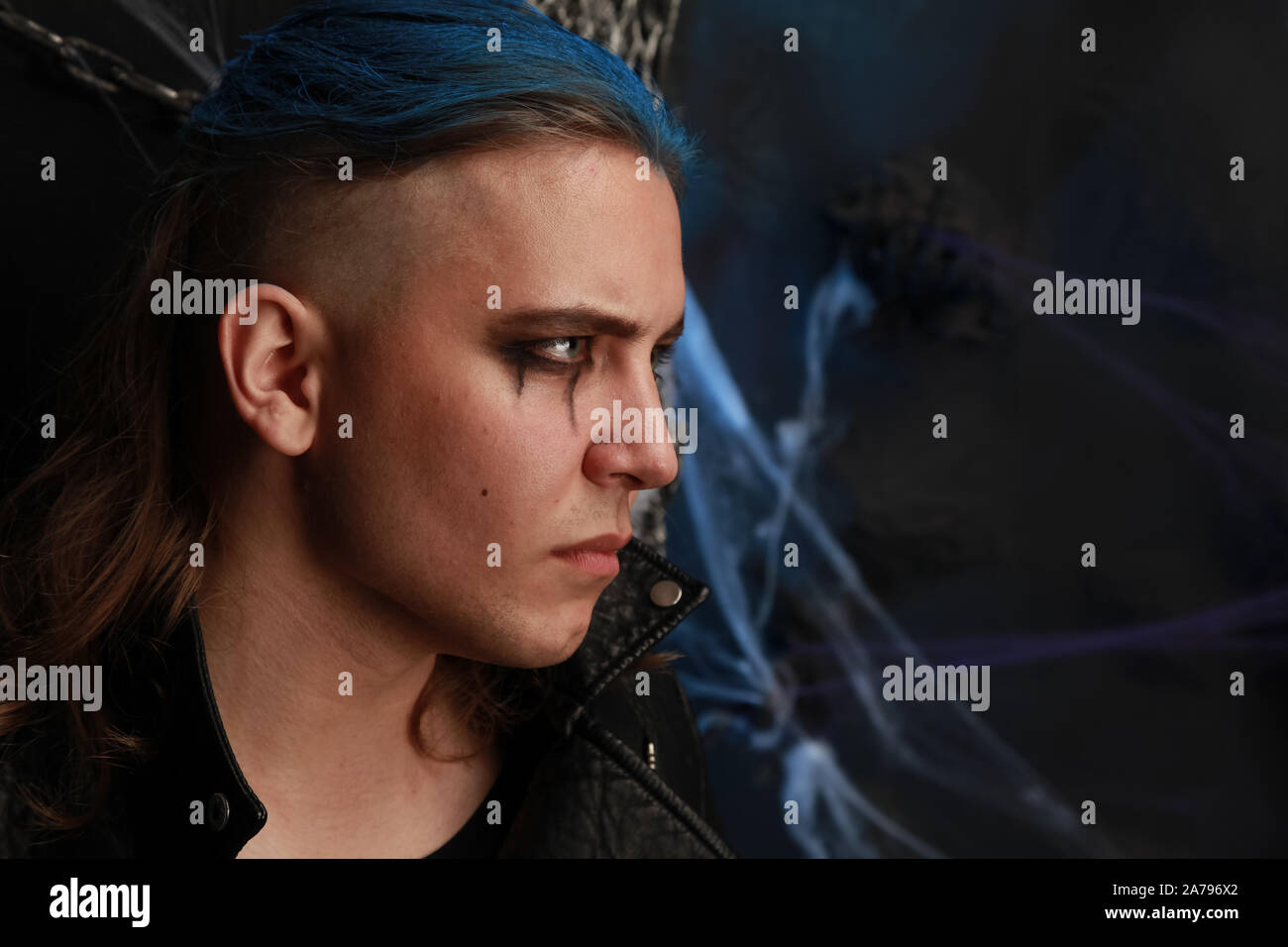 Teen alt boy with blue hair and shaved head dressed in black on dark ...