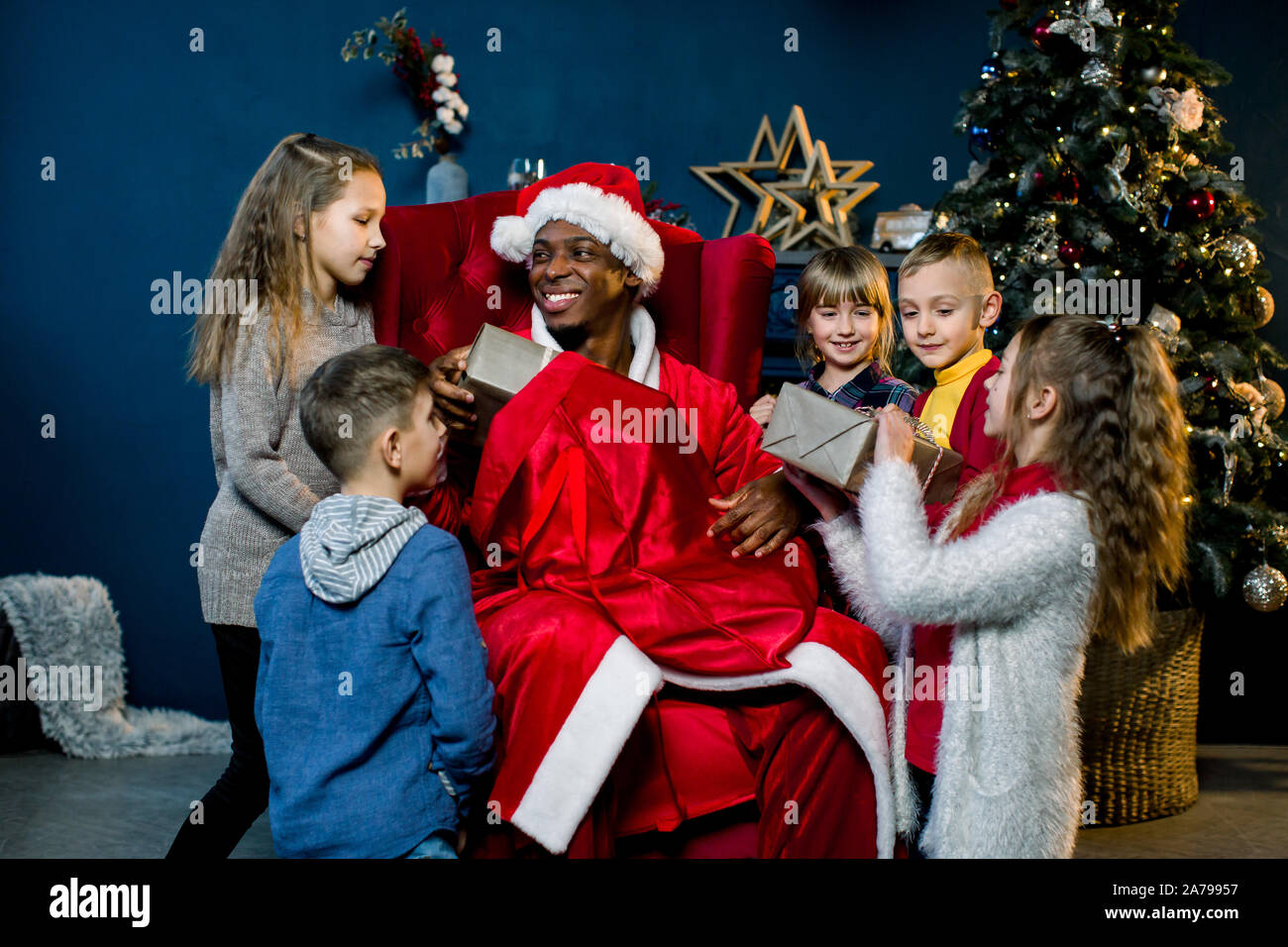 African Santa Claus is seated and gives presents to beautiful little ...