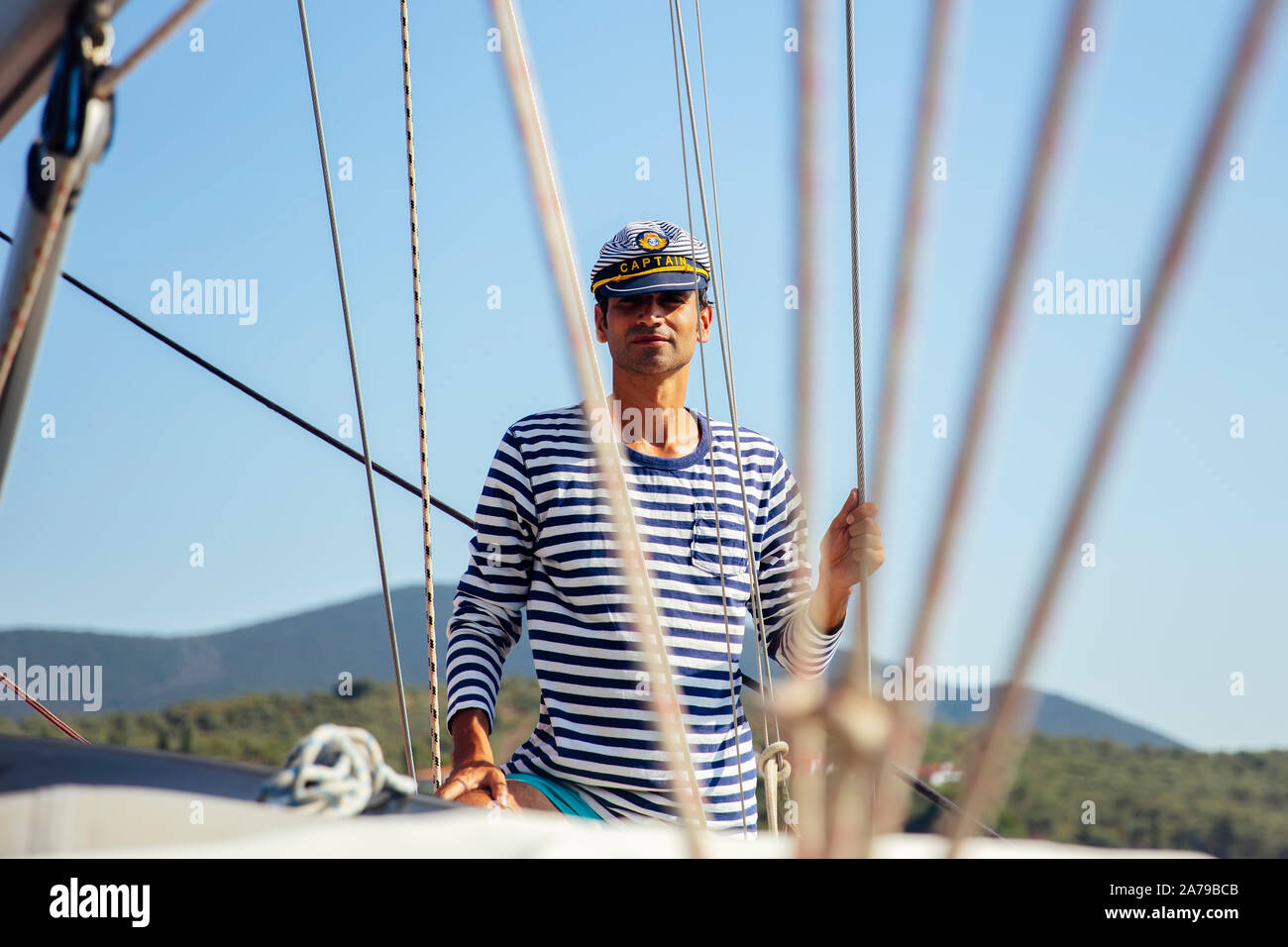 Handsome young man with captain cap on a sailboat at sea on a suuny day ...