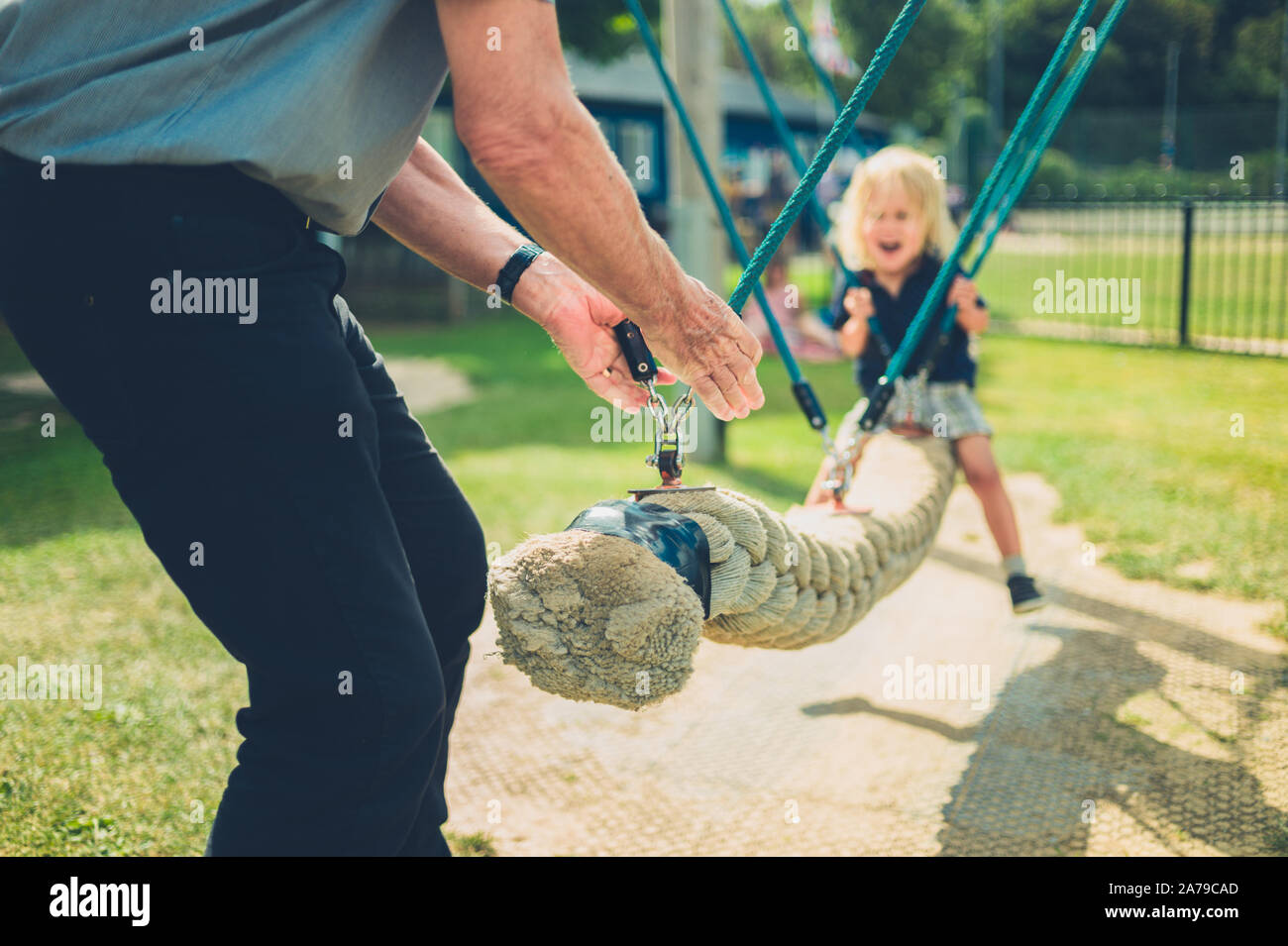 A little toddler is being pushed on a swing by his grandfather Stock ...