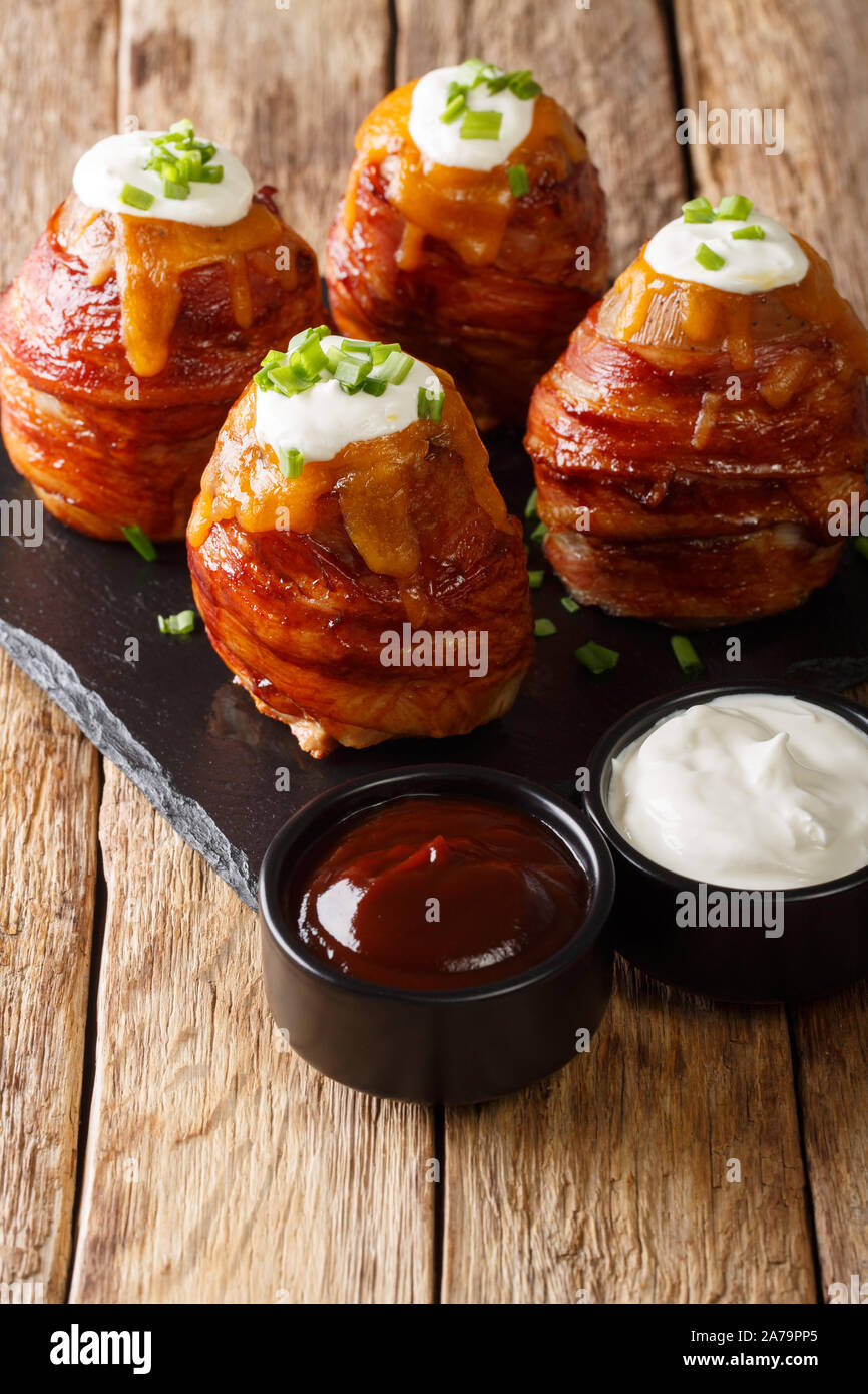 Grilled volcano potatoes wrapped in bacon topped with cheese and sour cream close-up on the ...