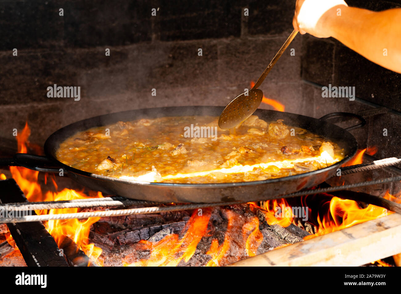 homemade paella making of, burning in fireplace fire with hand holding ...