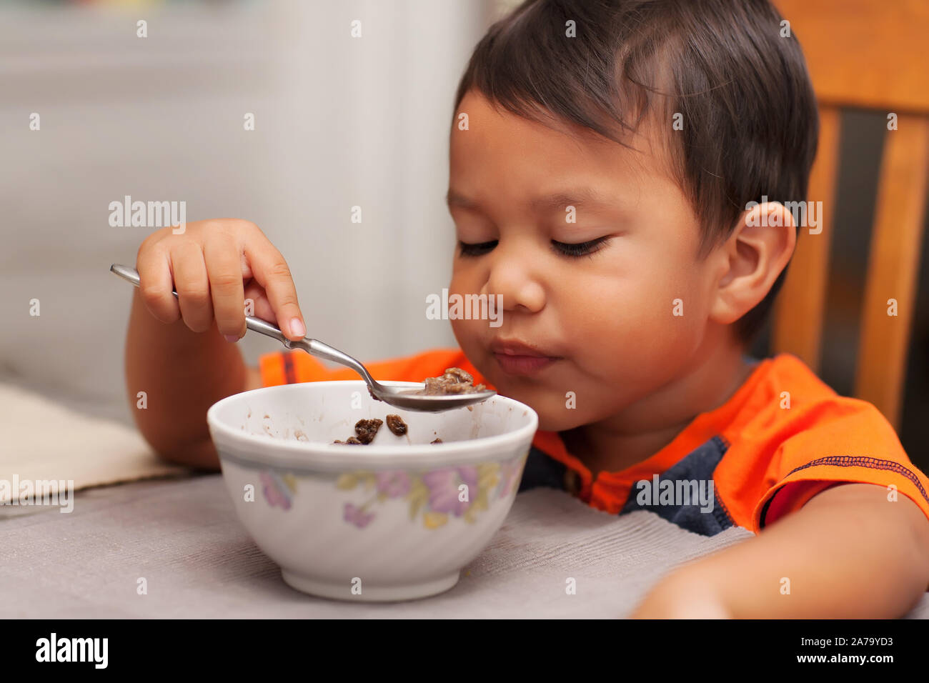 Cute young boy holding a spoonful of cereal and staring at the food ...