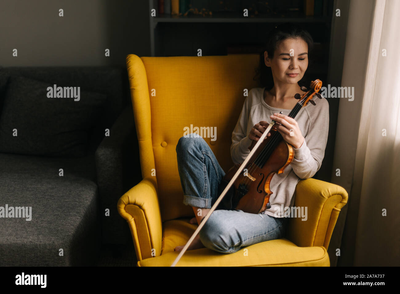 Pretty violinist woman sits with a violin in a soft chair at home Stock ...