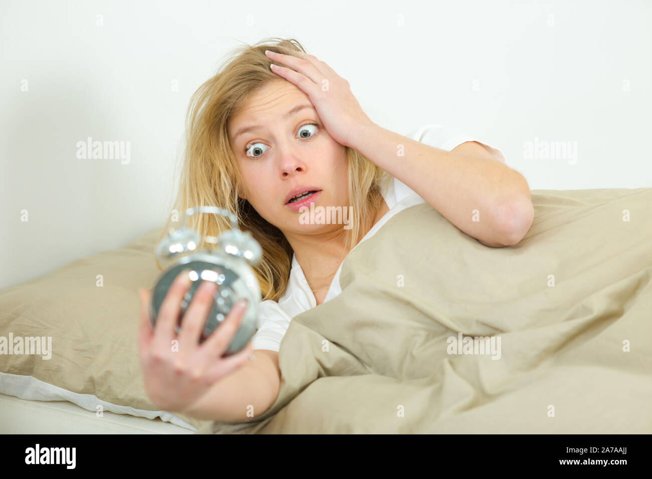 woman in bed looking at alarm clock with shcoked expression Stock Photo ...