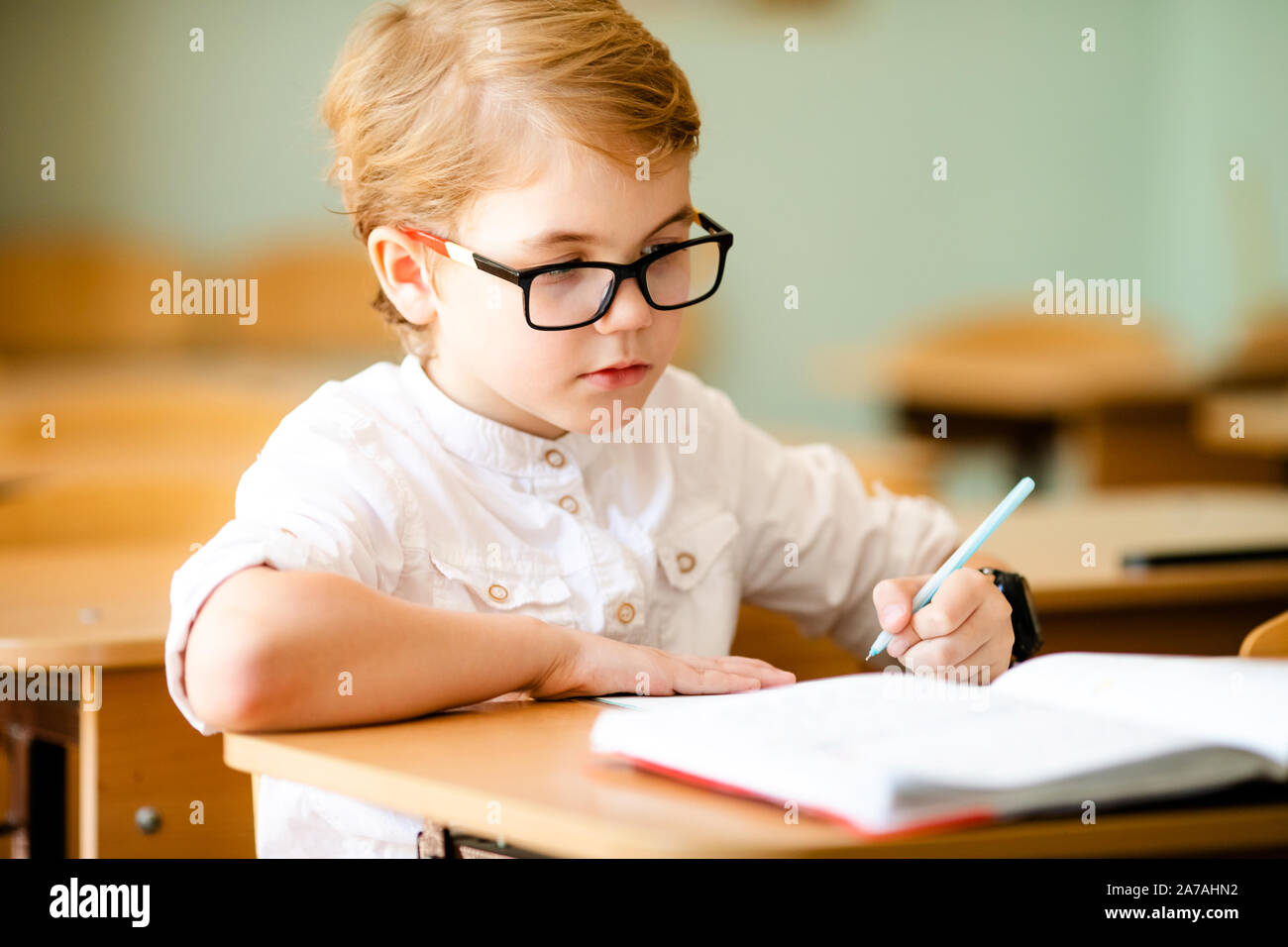 Seven years old child with glasses writing his homework at school. Boy ...