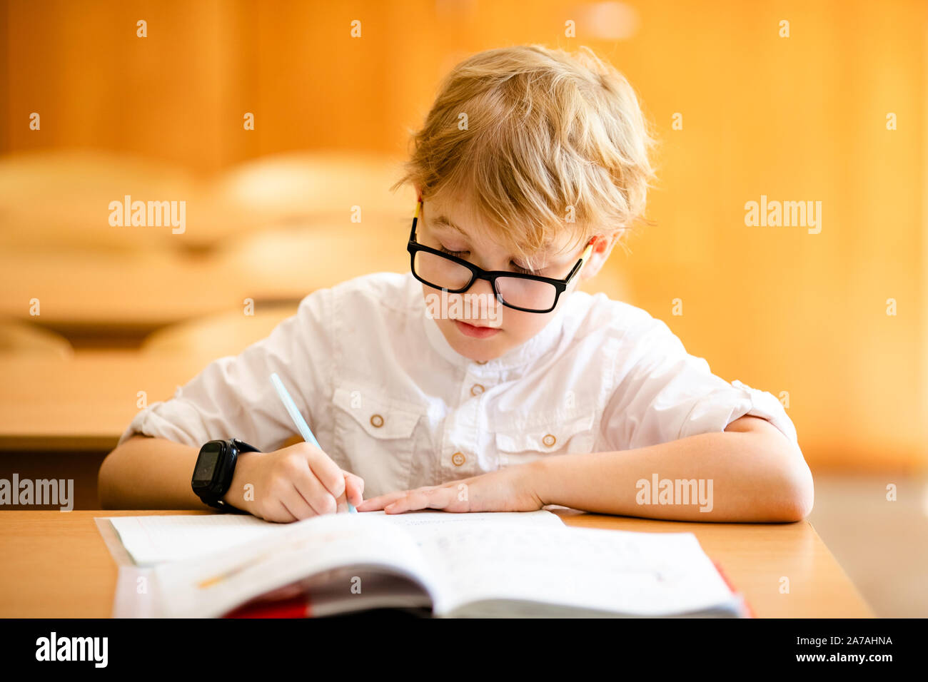 Seven years old child with glasses writing his homework at school. Boy ...