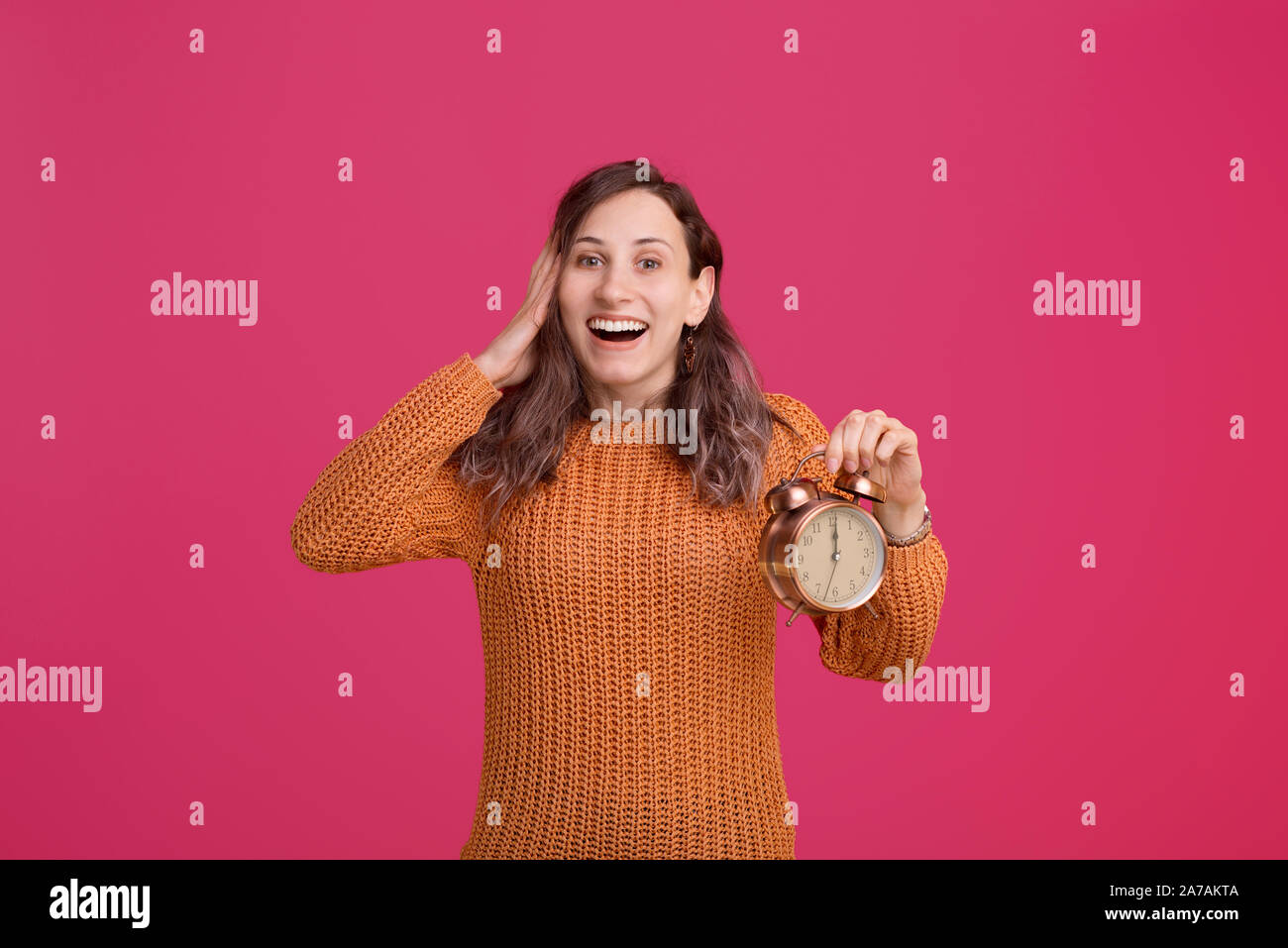 Photo of surprised young woman holding alarm clock over pink background ...