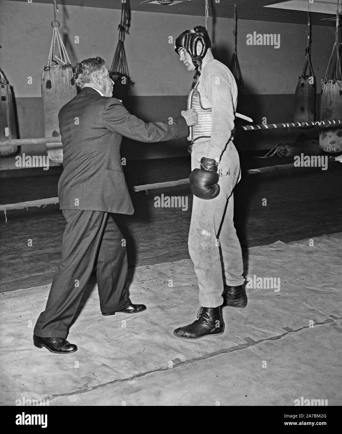 Man in a suit throwing a punch at the torso of a boxer in a ring ca ...