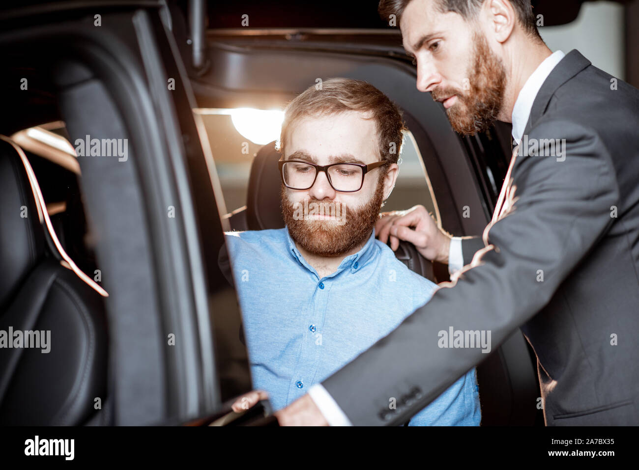 Sales manager showing vehicle interior for a young customer at the back ...