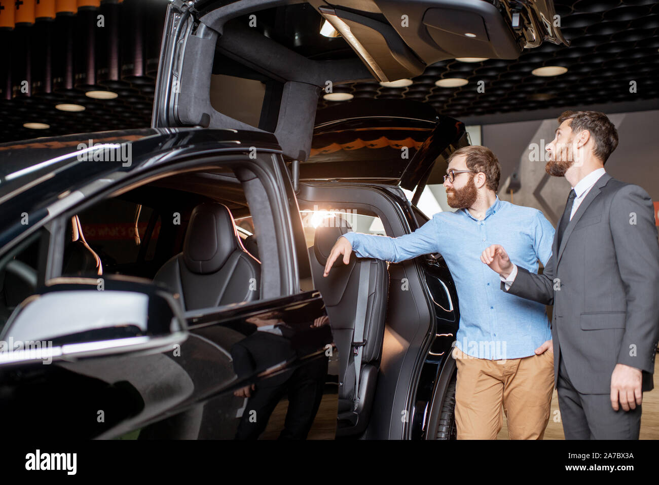 Sales manager showing vehicle interior for a young customer at the back ...