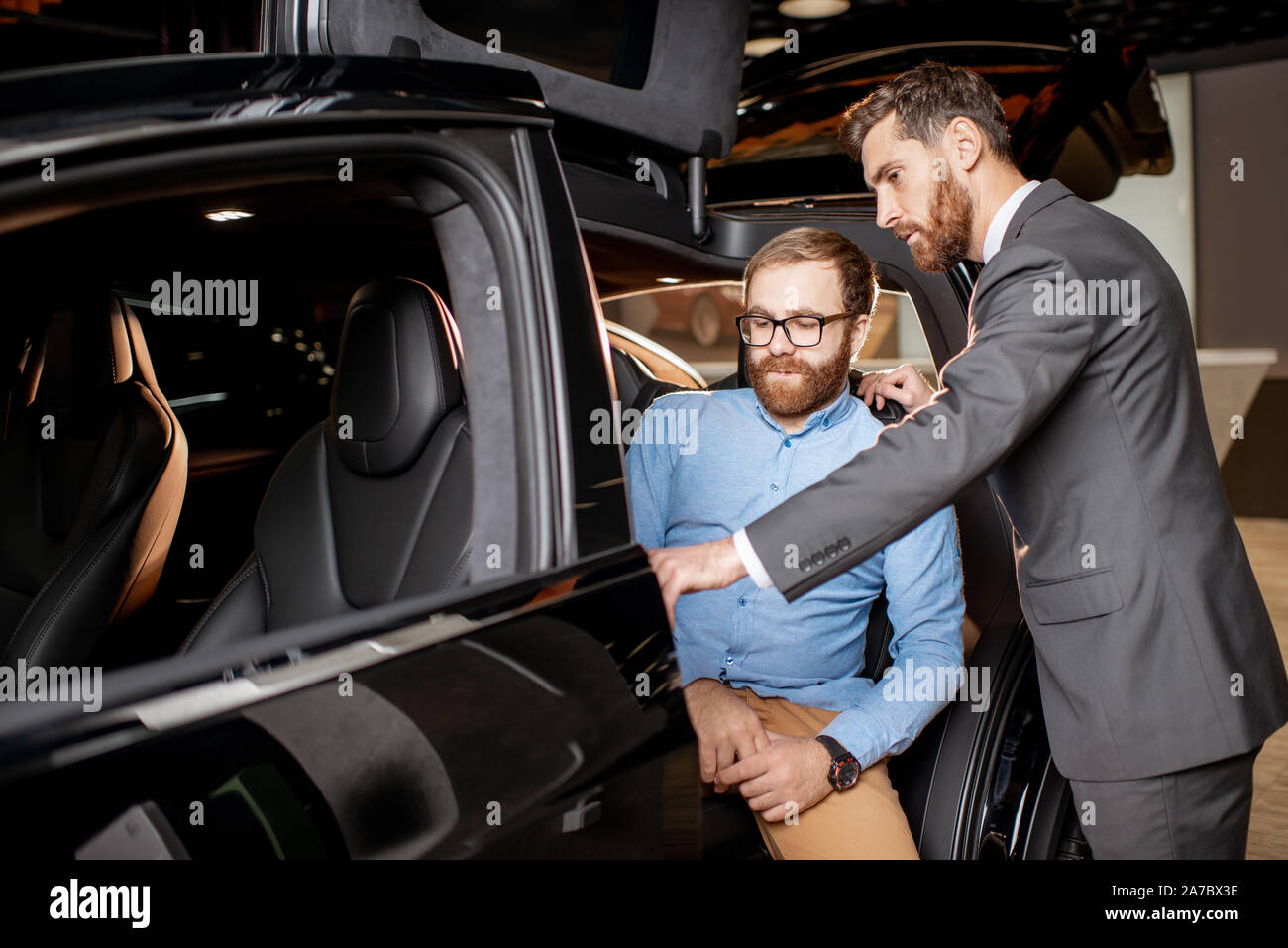 Sales manager showing vehicle interior for a young customer at the back ...