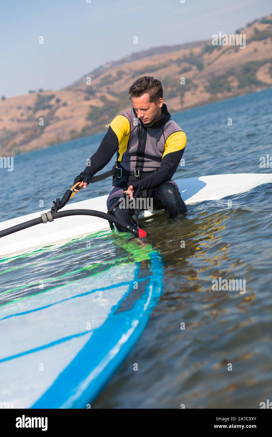 Portrait of windsurfer preparing his equipment while sitting on board ...