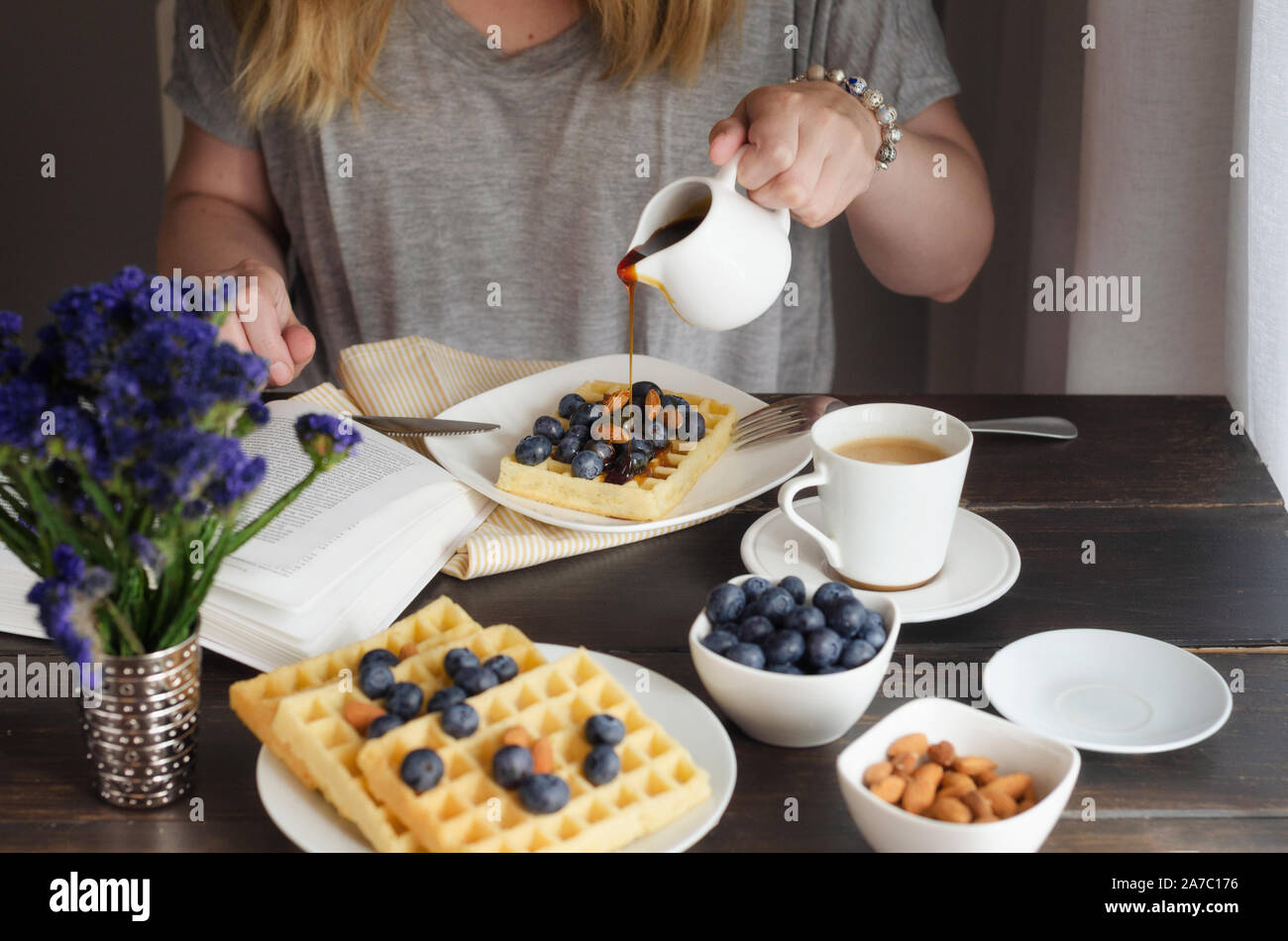 Girl pouring syrup over belgian waffle decorated with blueberries and ...