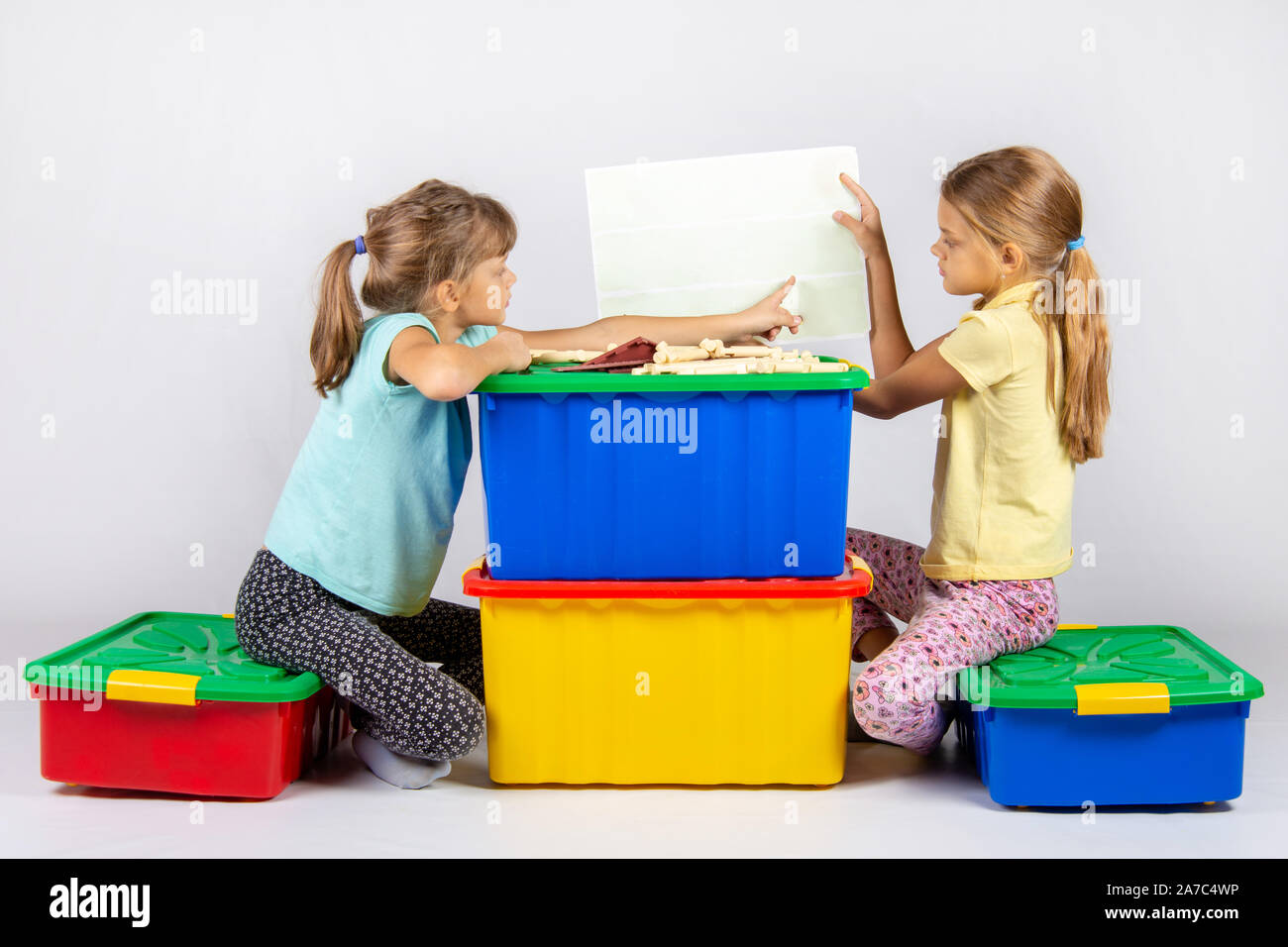 Two girls sit on large toy boxes and look at the toy assembly ...