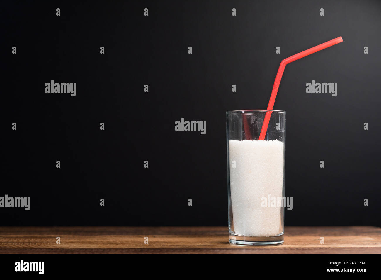 A glass full of white sugar with straw against black background ...